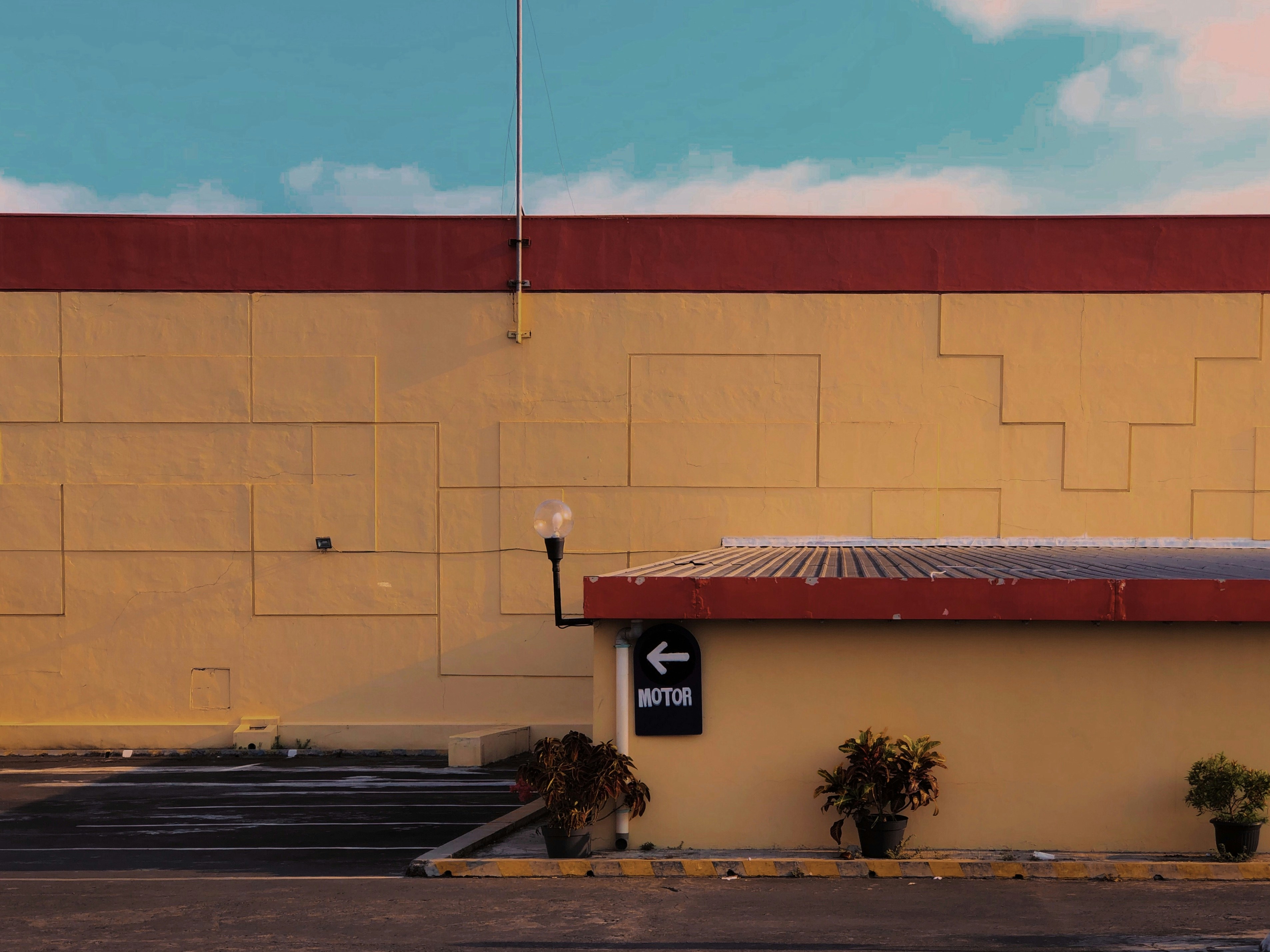 Bright yellow wall of a building with geometric patterns, featuring a sign pointing left and potted plants in front.
