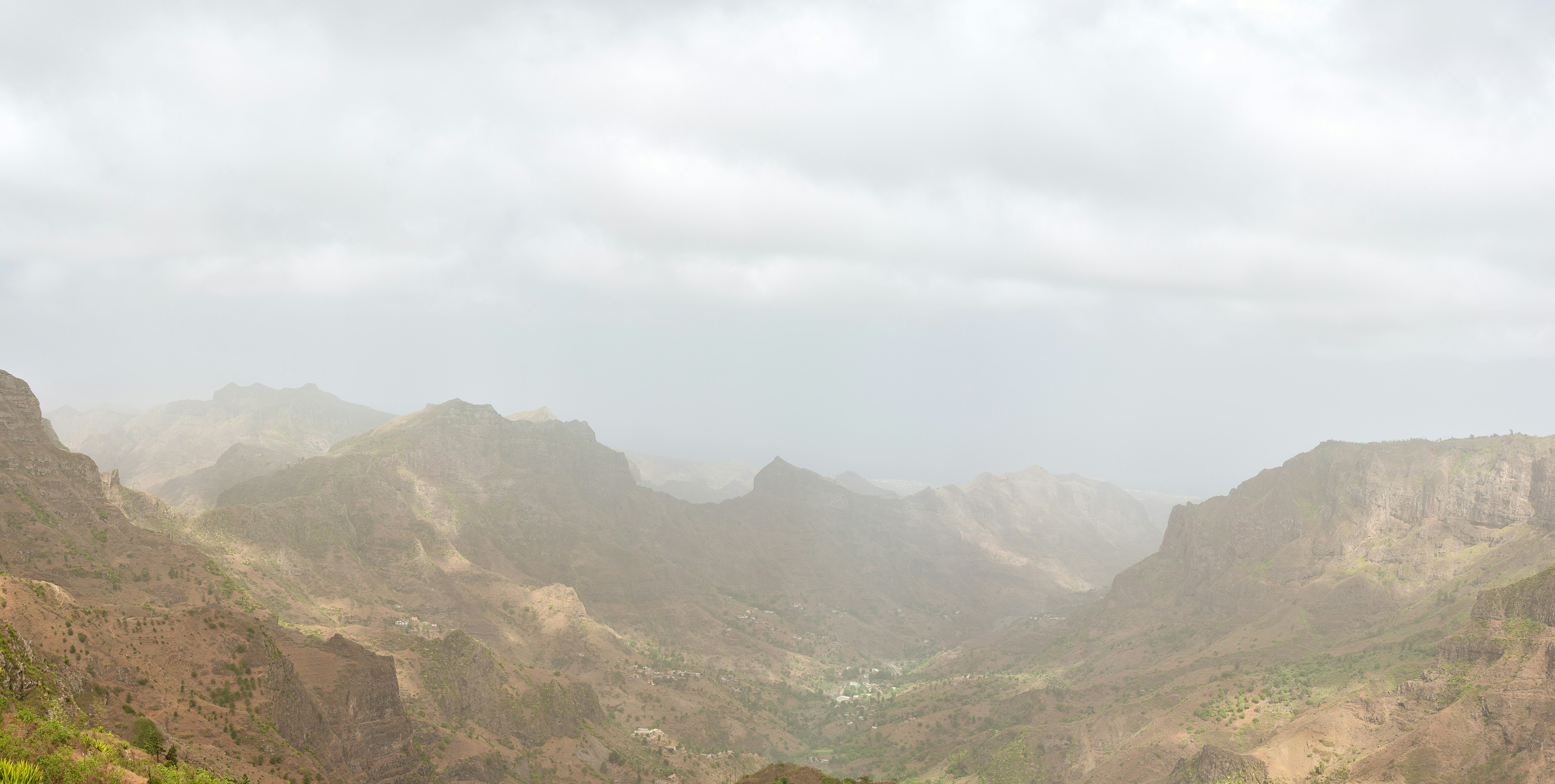 Rolling green and brown mountains under a cloudy white sky during daytime.