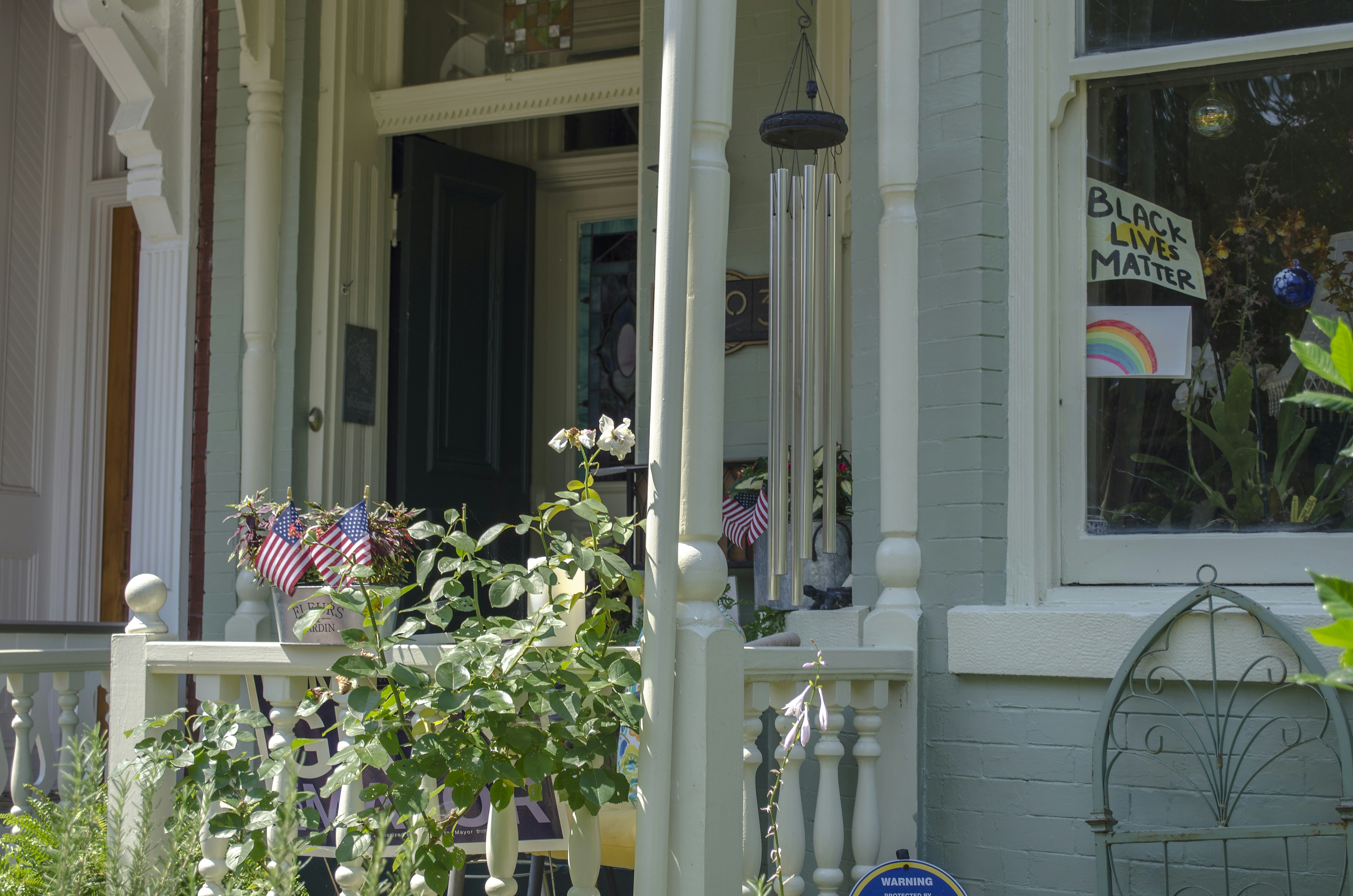 Charming porch adorned with plants and American flags, featuring a window sign advocating for social justice.