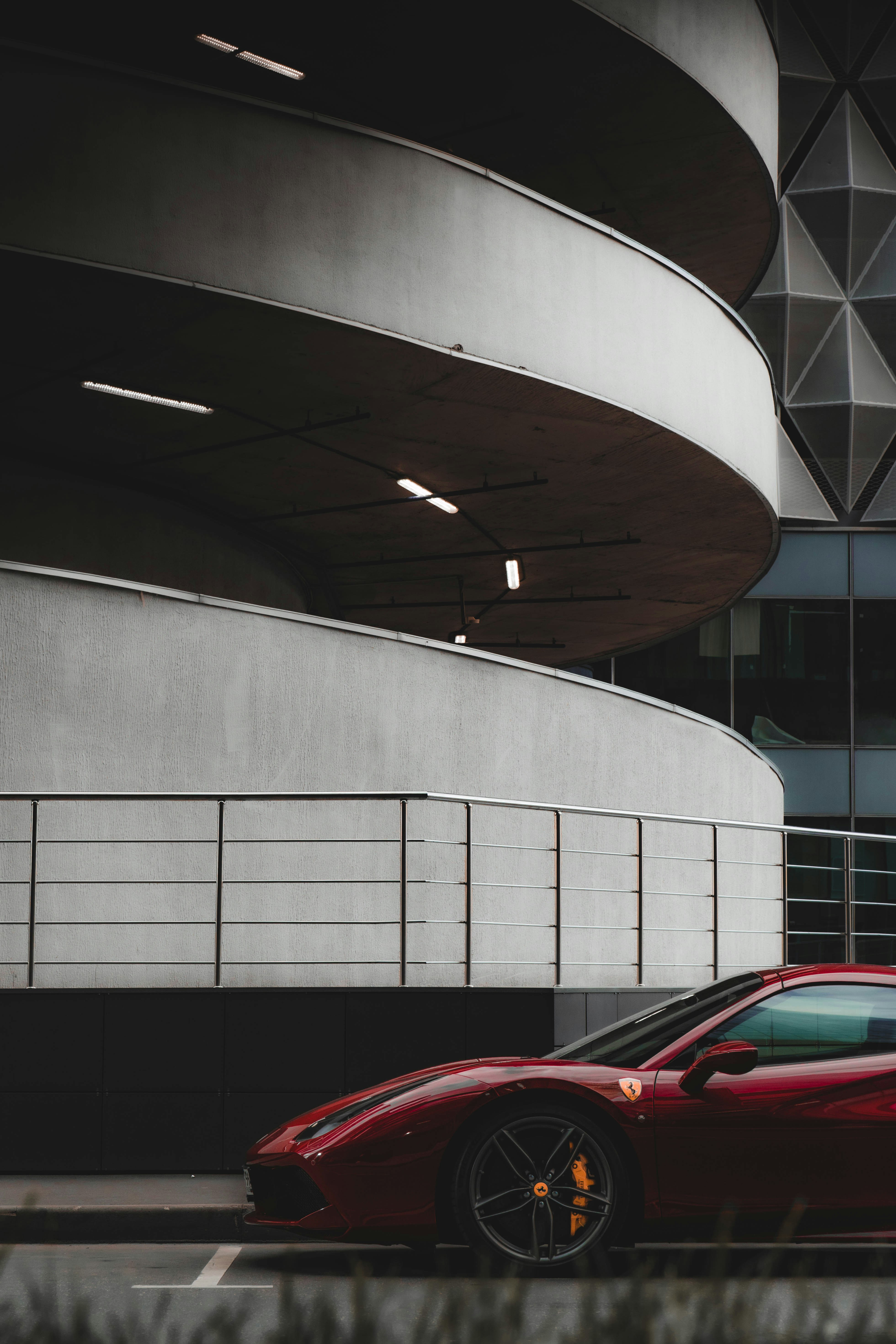 Red sports car parked beside a spiral parking structure, emphasizing modern architecture and automotive design.