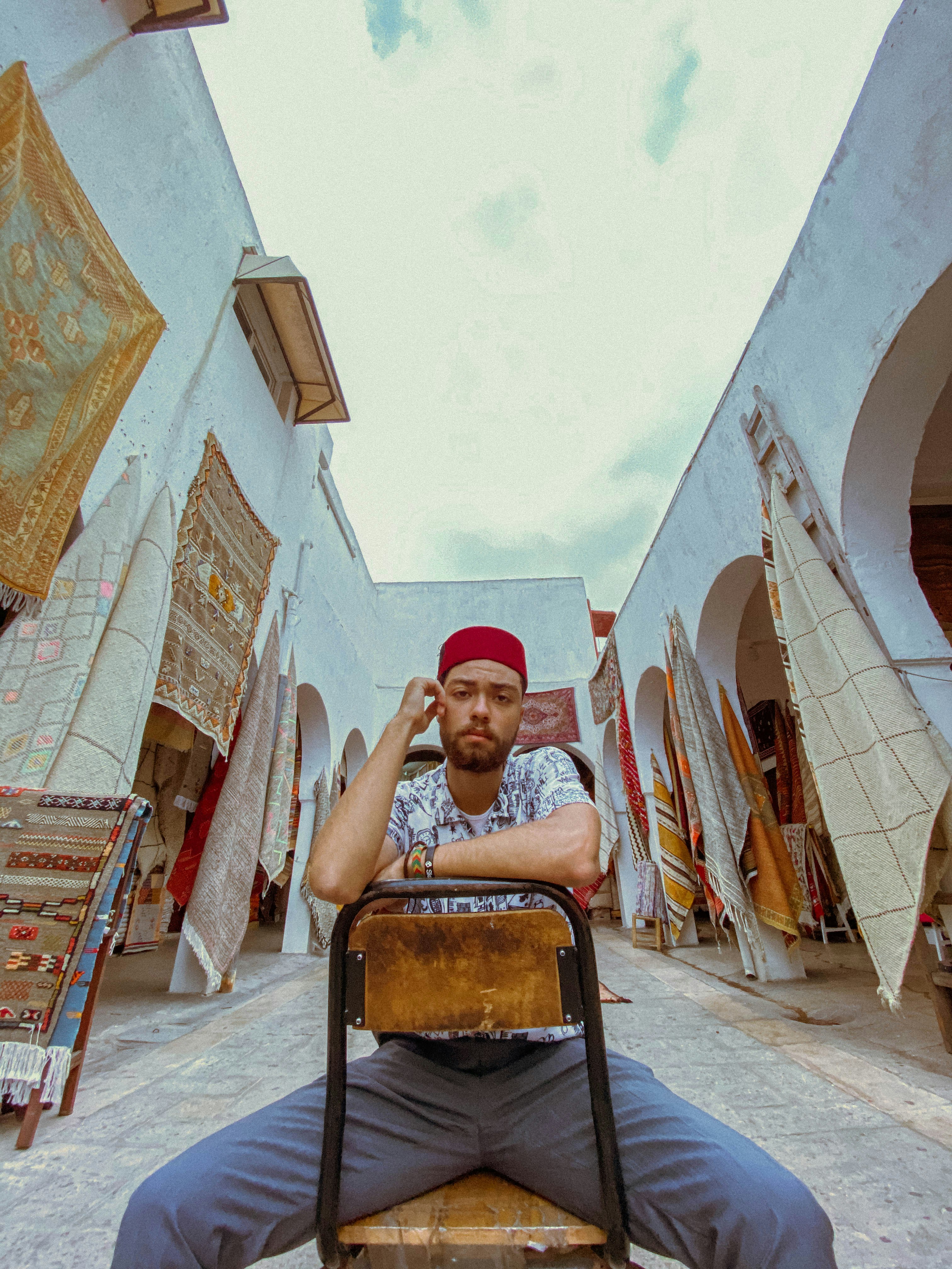 Red Fez in the Courtyard: A Casual Portrait Amid Arches and Textiles
