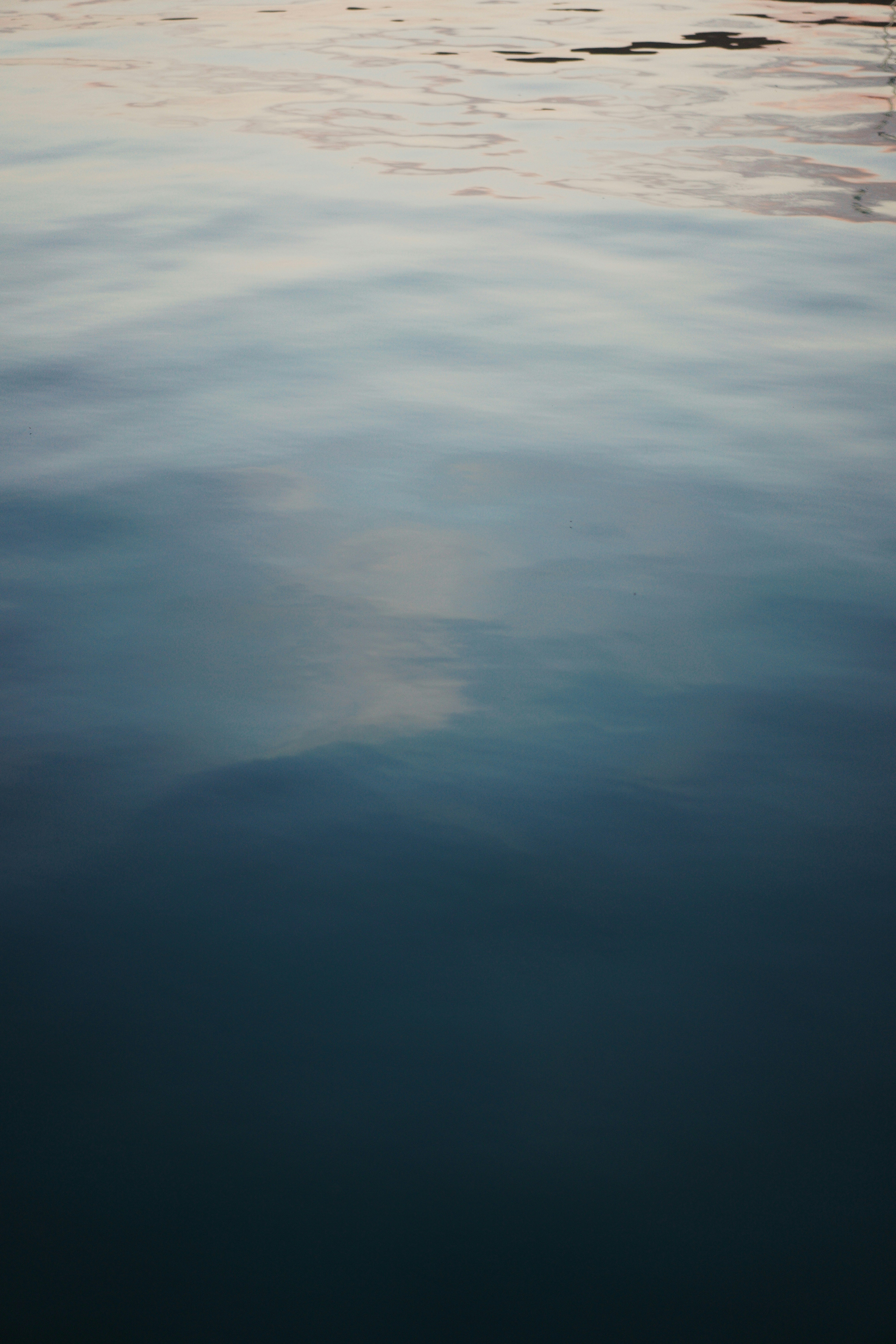Calm water surface reflecting soft hues of twilight, creating a tranquil atmosphere.