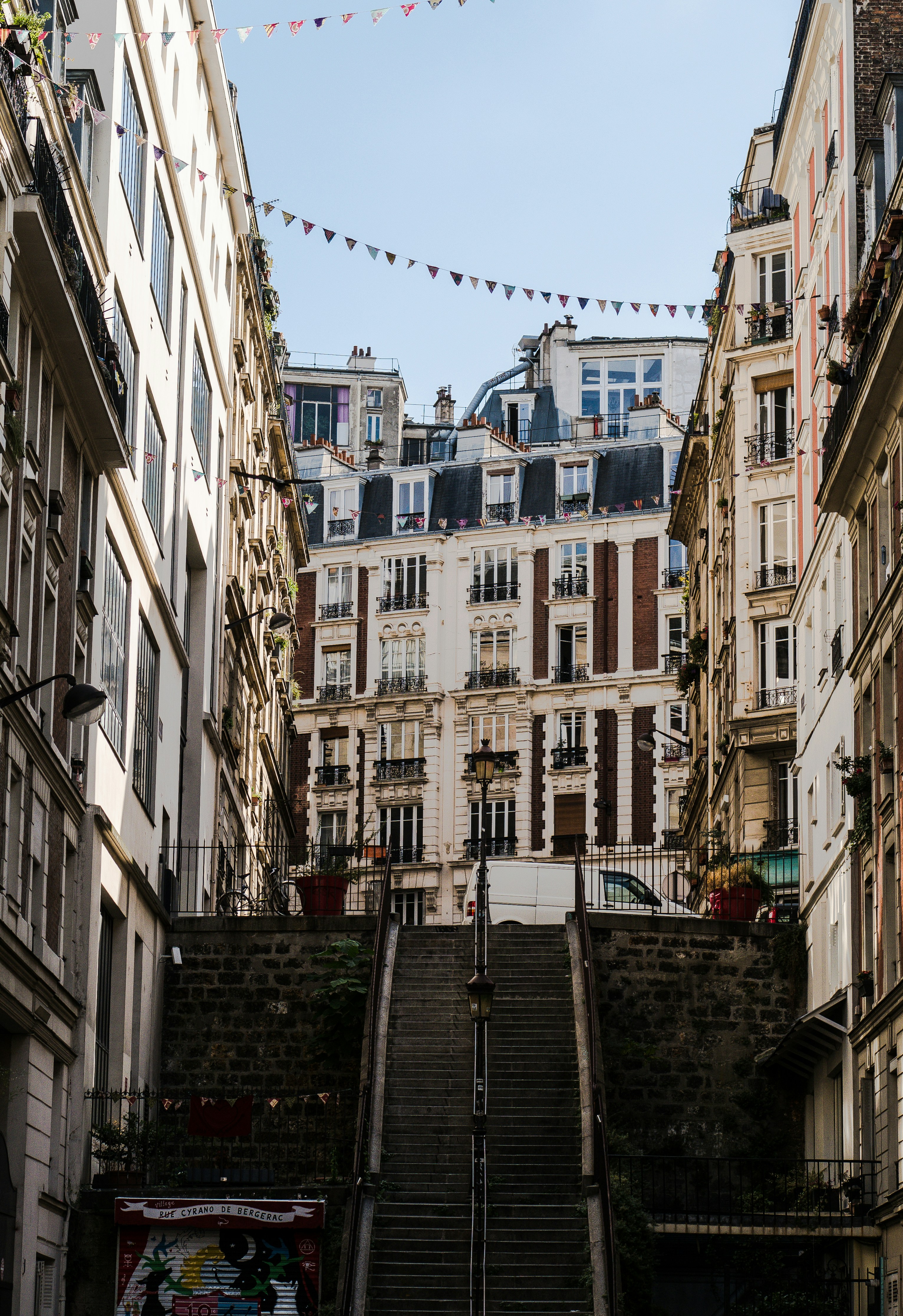 A vibrant street scene showcasing a staircase framed by buildings adorned with colorful bunting, leading to a picturesque Parisian facade.