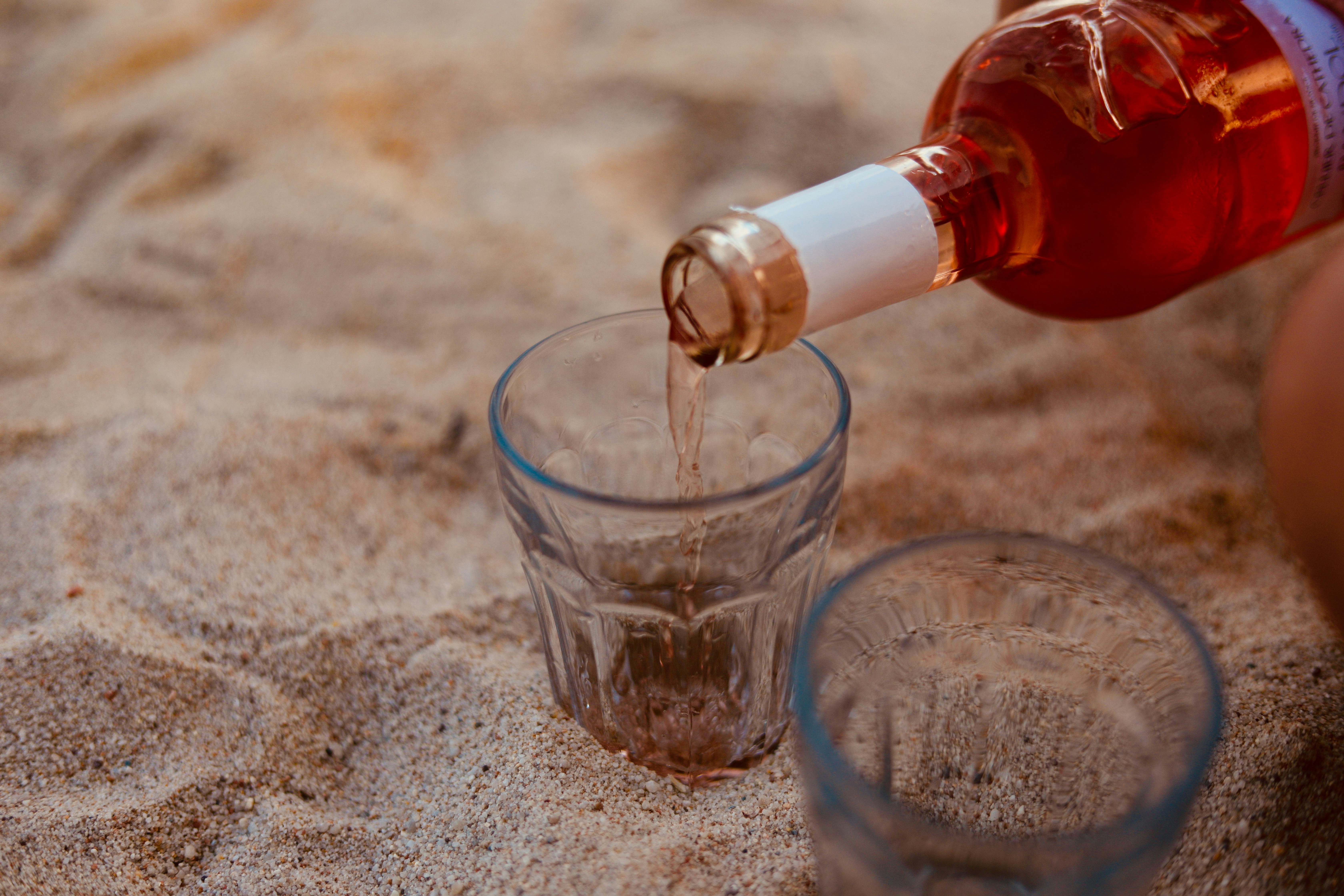 Rosé wine being poured into a glass on a sandy beach, capturing a moment of relaxation and enjoyment.