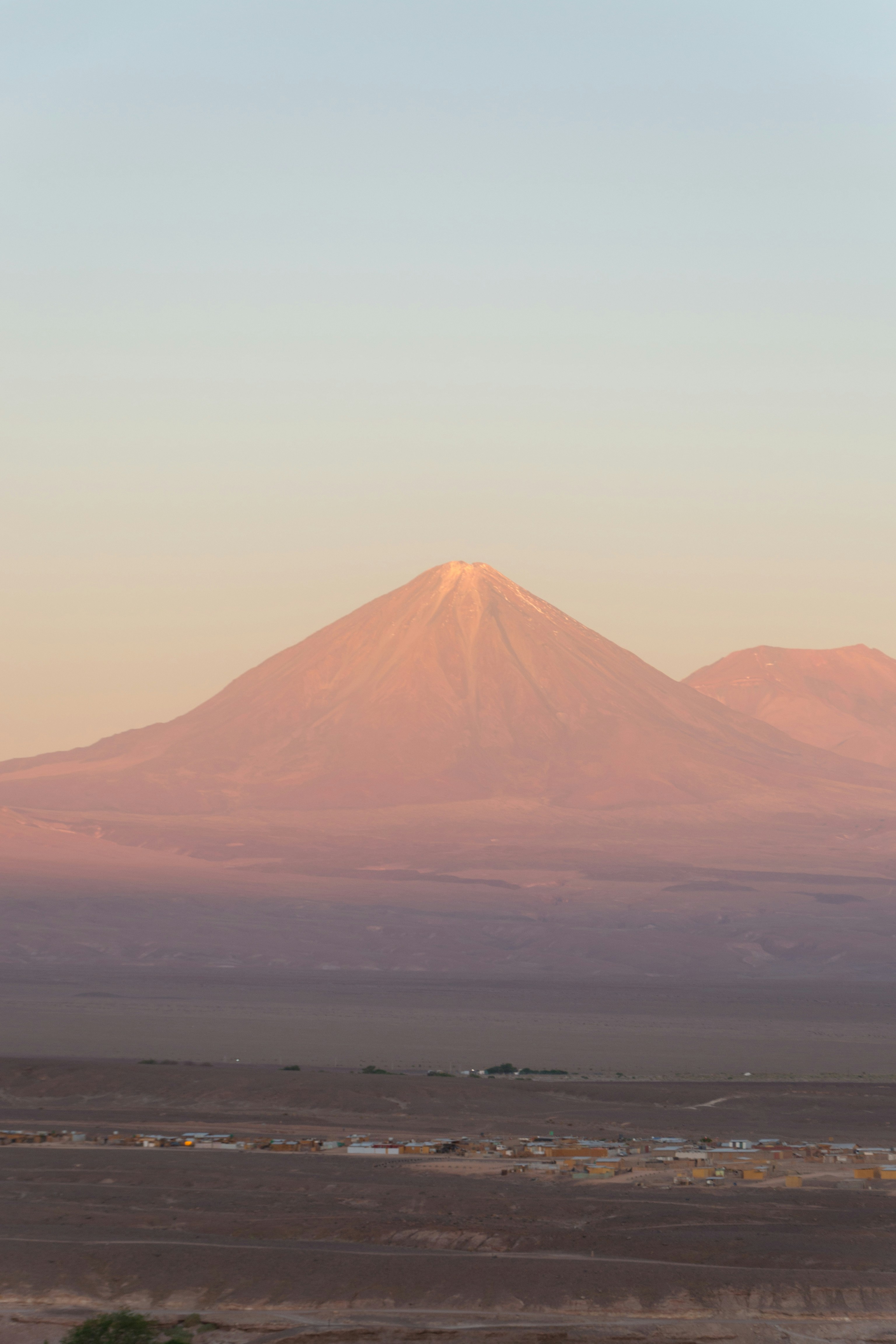 Majestic volcano rising against a pastel sky, casting a serene presence over the arid landscape below.