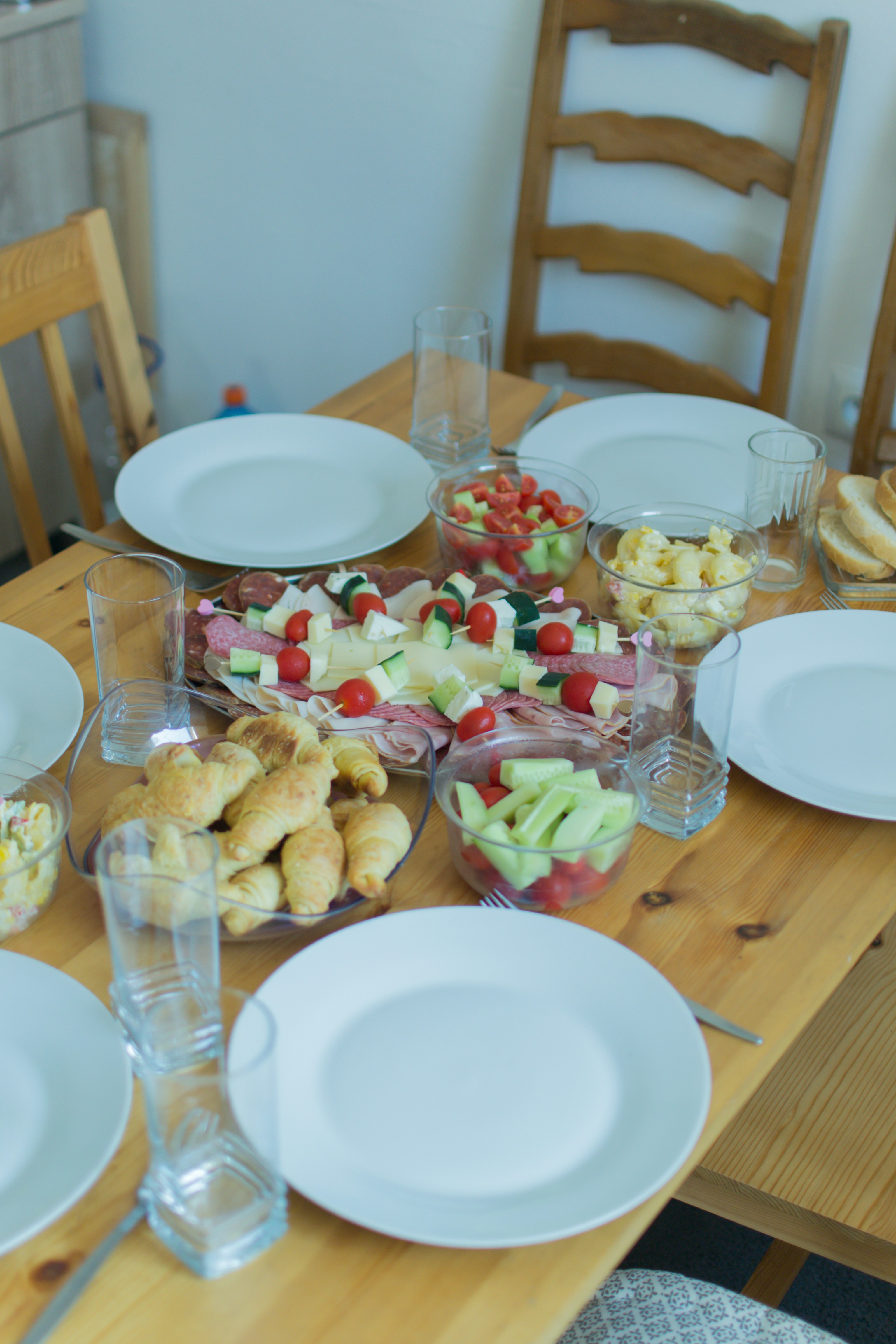 A beautifully arranged table featuring a variety of dishes, including fresh vegetables, croissants, and salads, inviting guests to enjoy a delightful meal.