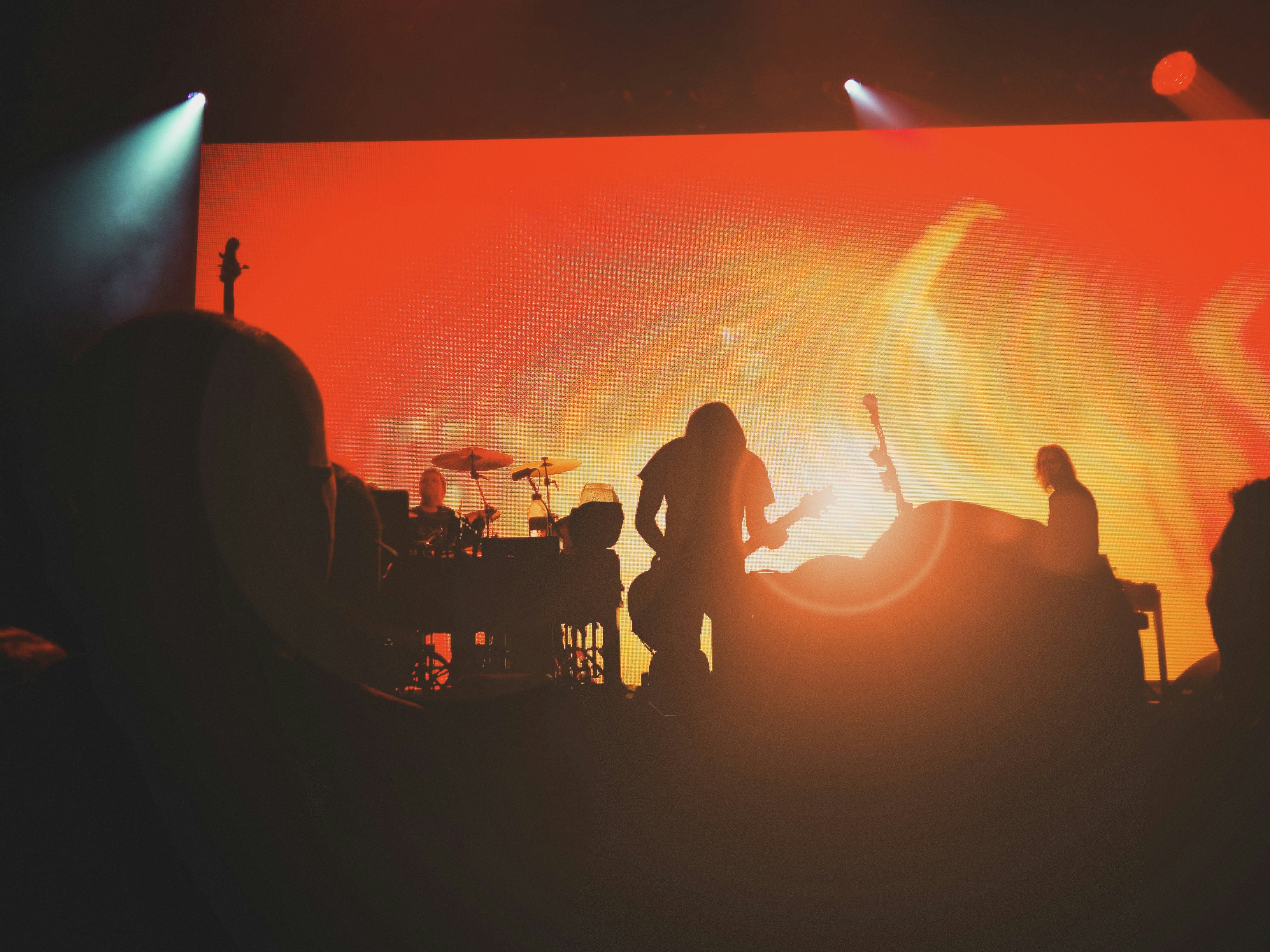 Silhouetted musicians perform against a vibrant, orange-lit backdrop.