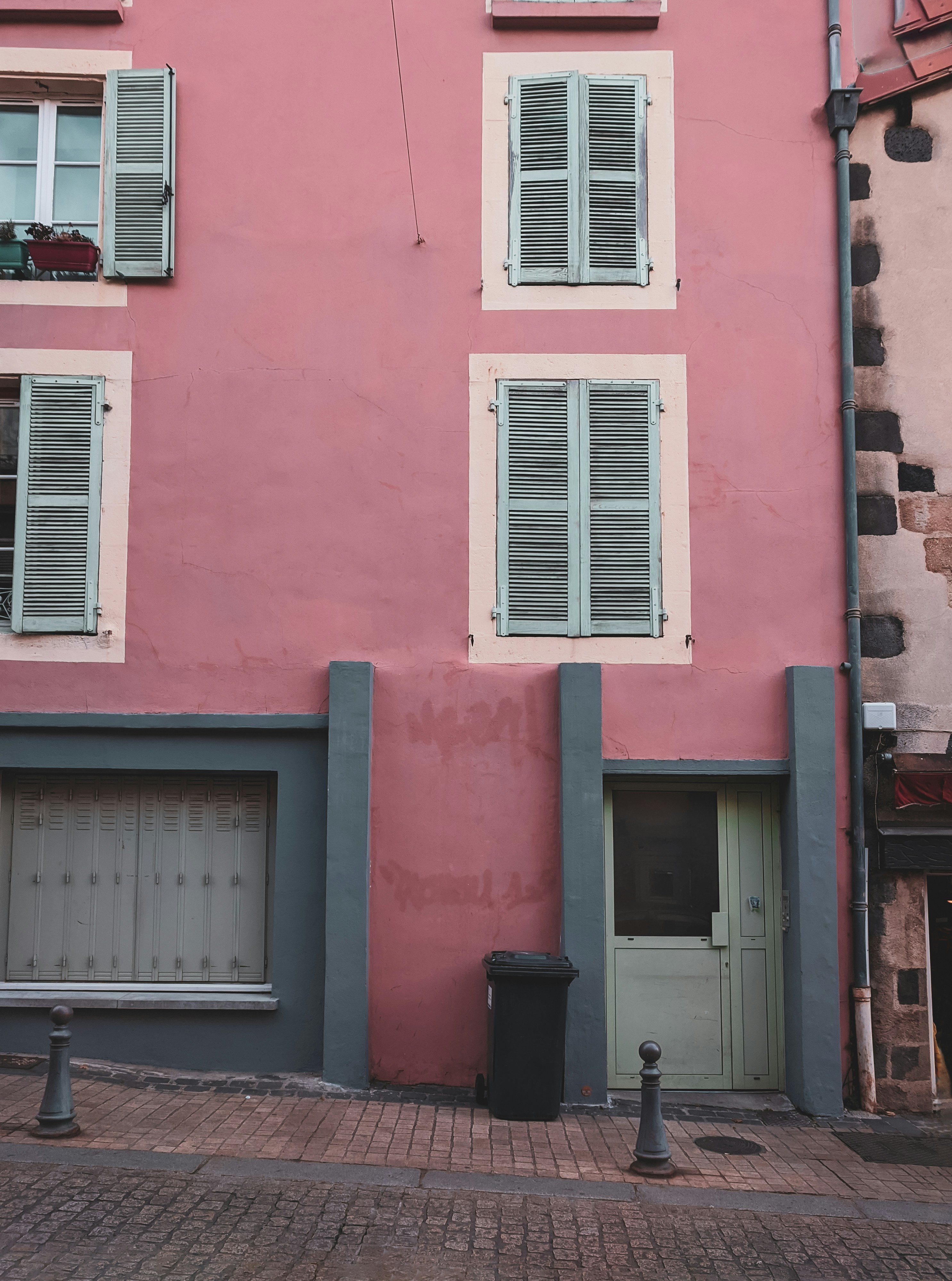 Pastel Facade: A Quiet Pink Streetfront Framed by Shutters and a Pale Green Door