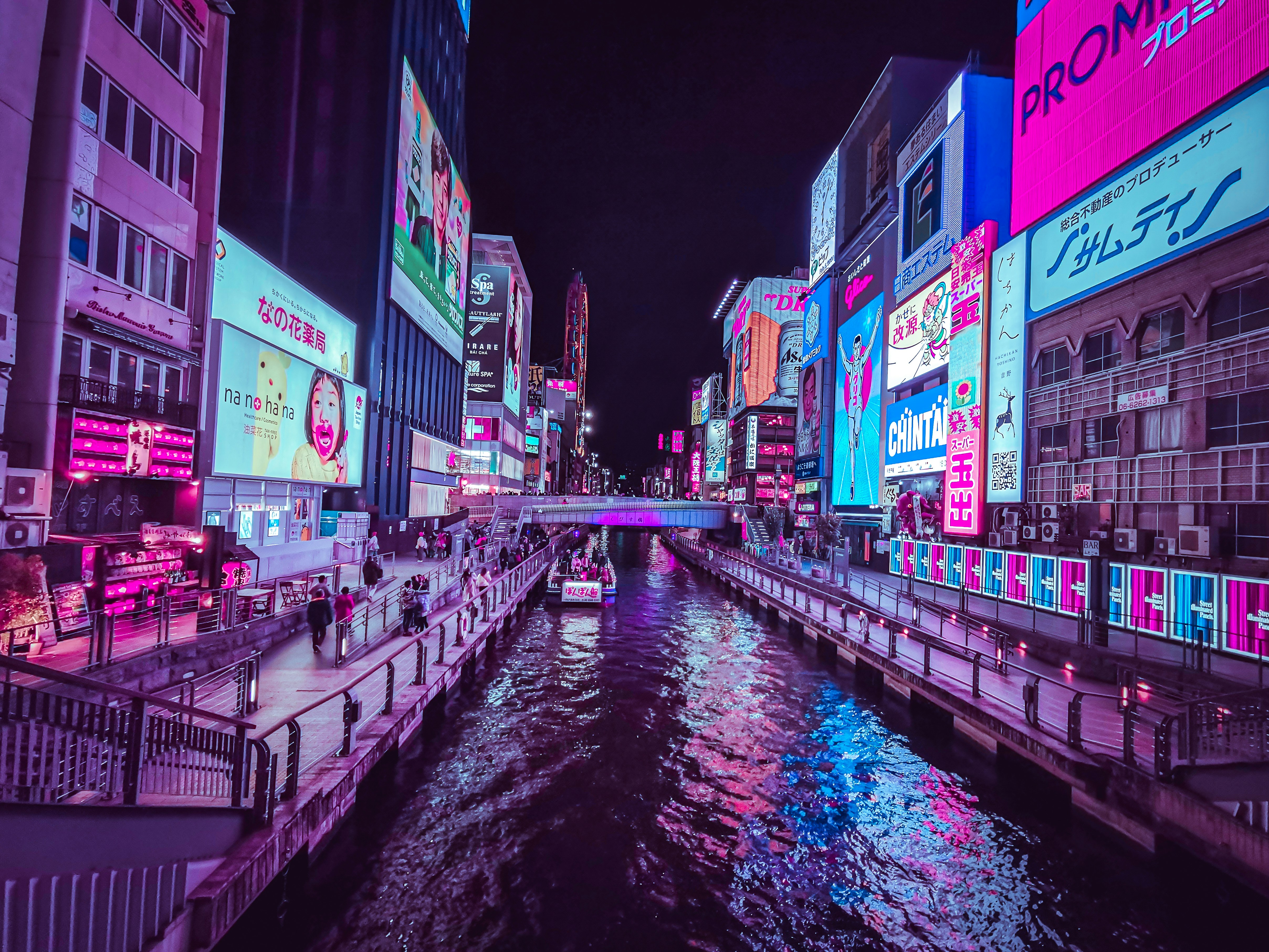 Vibrant cityscape featuring illuminated billboards along a canal, with reflections shimmering on the water's surface.