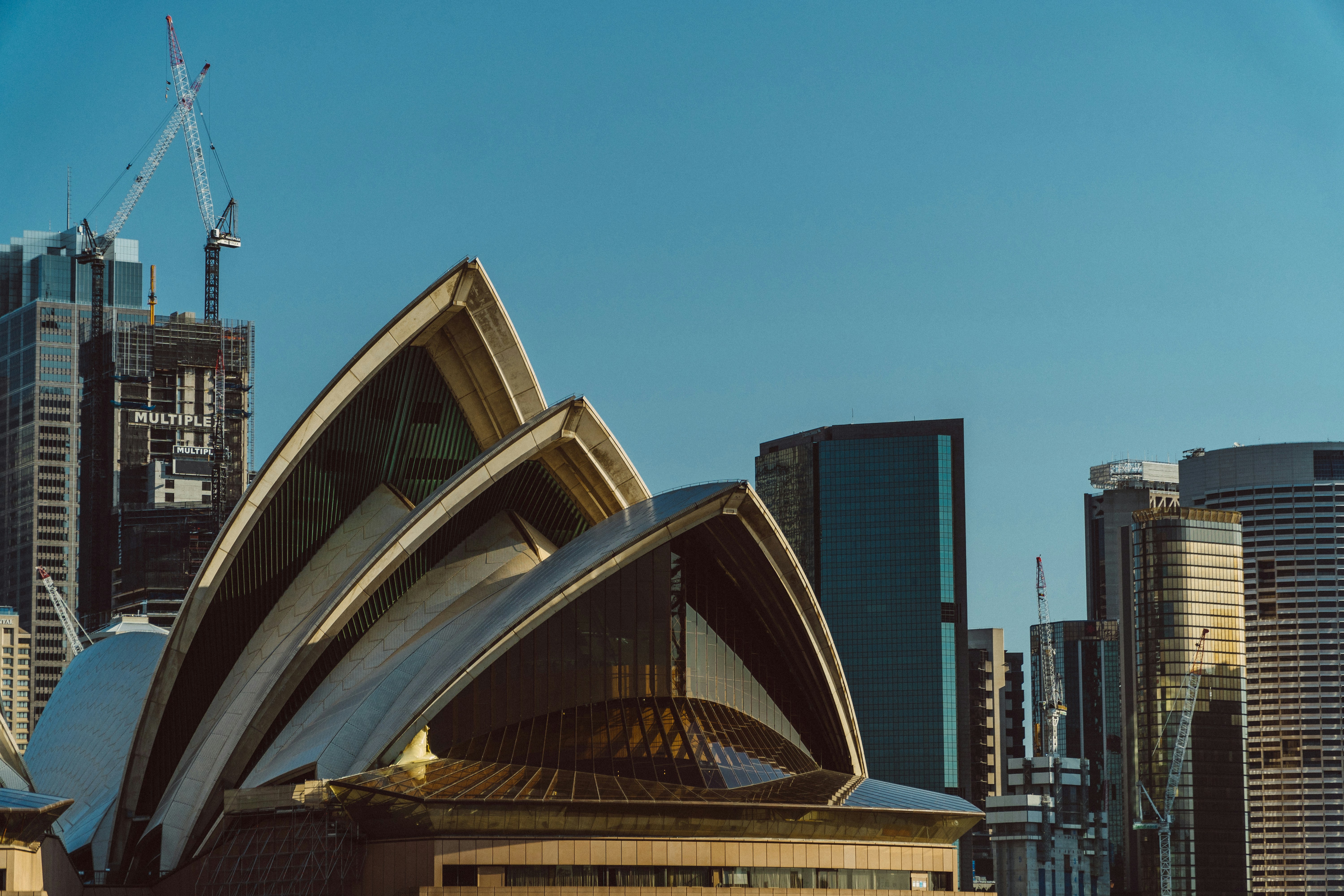 Sydney Opera House juxtaposed against modern skyscrapers under a clear blue sky.