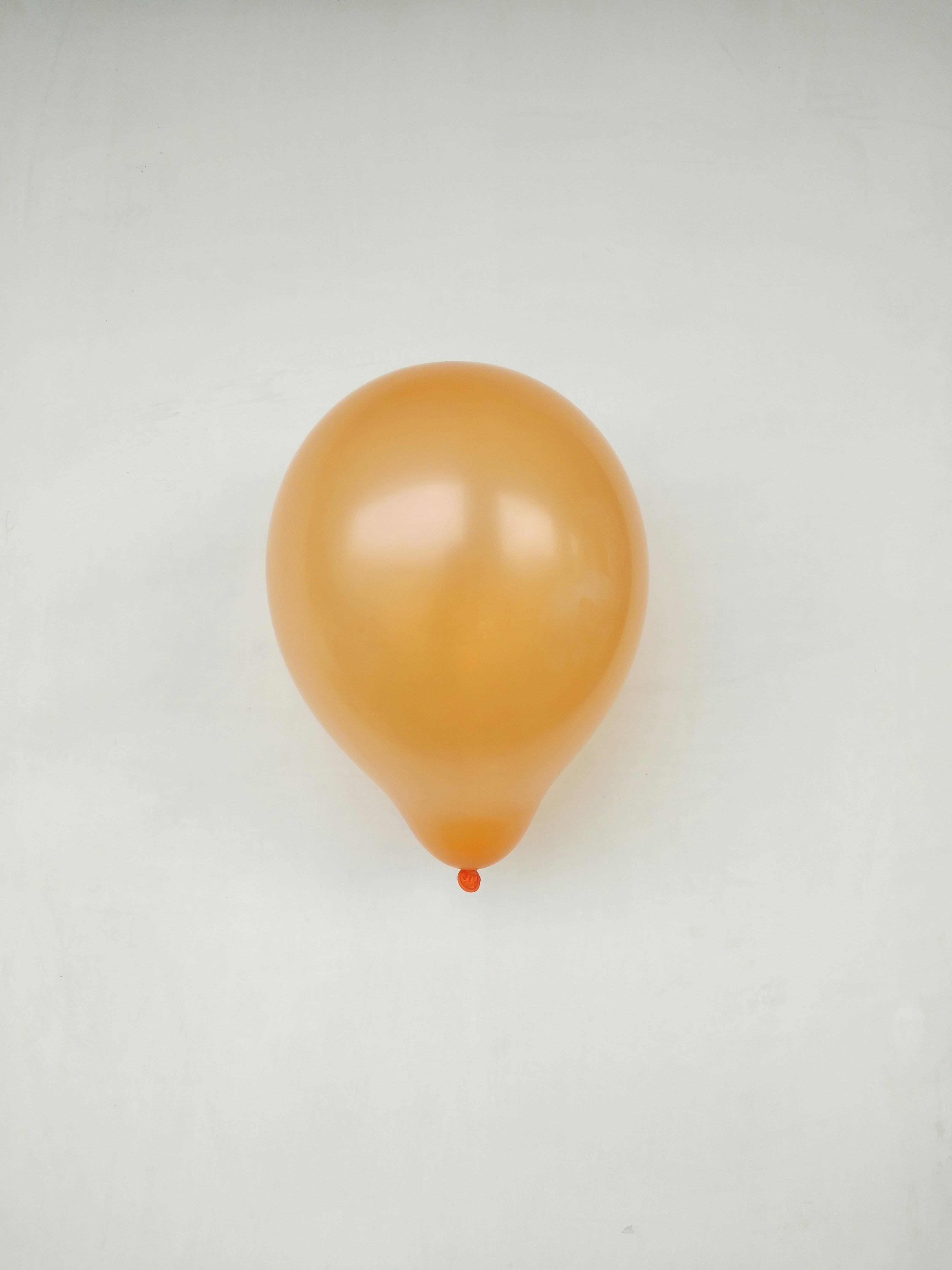 A smooth orange balloon gently suspended against a minimalistic white background.