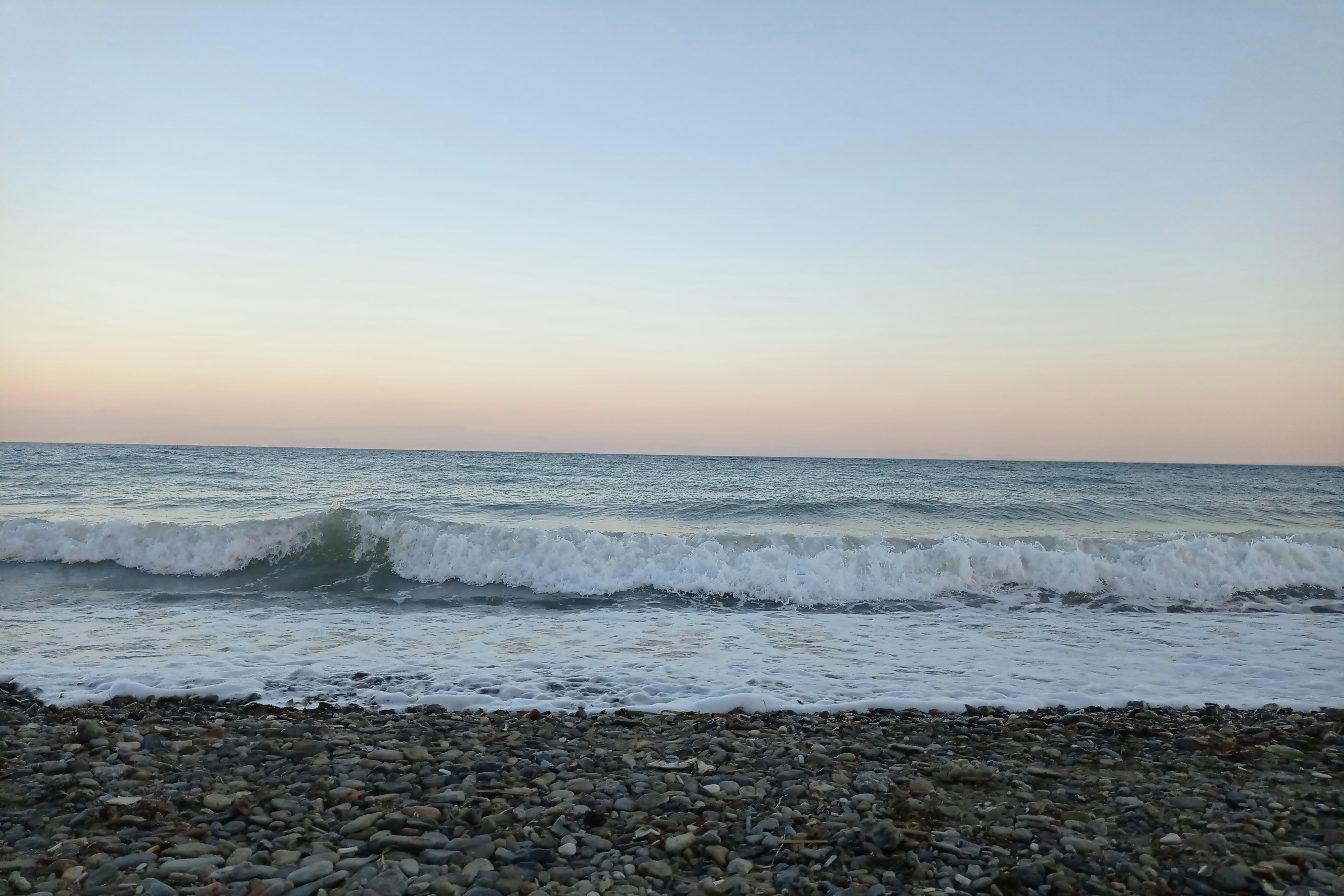 Gentle ocean waves lapping against a pebble-covered shore under a serene twilight sky.
