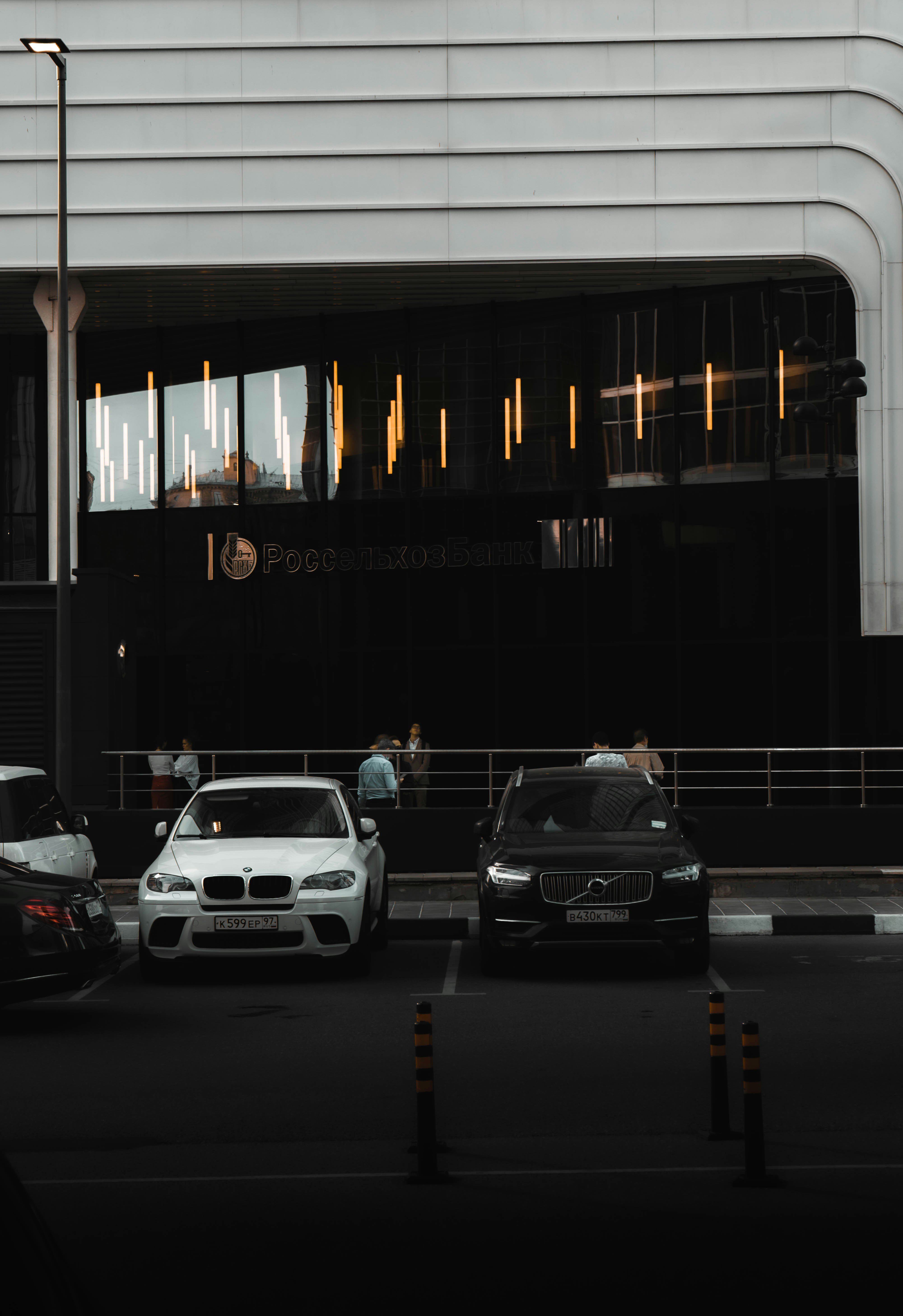 Modern bank facade with illuminated signage and sleek vehicles parked in front, capturing a blend of architecture and urban life.