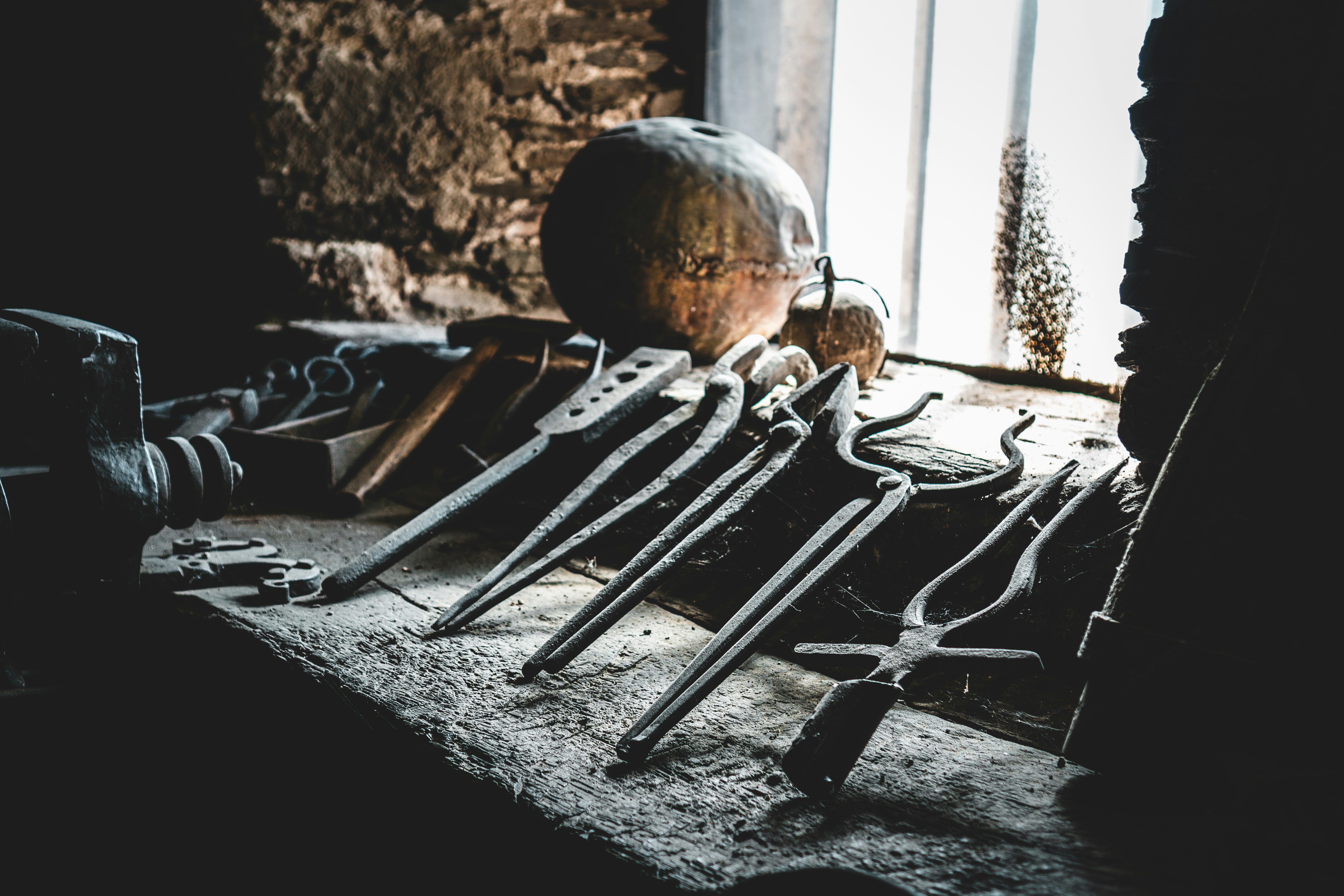 Rustic tools arranged on a weathered surface, illuminated by soft light streaming through a window. The scene evokes a sense of history and craftsmanship.