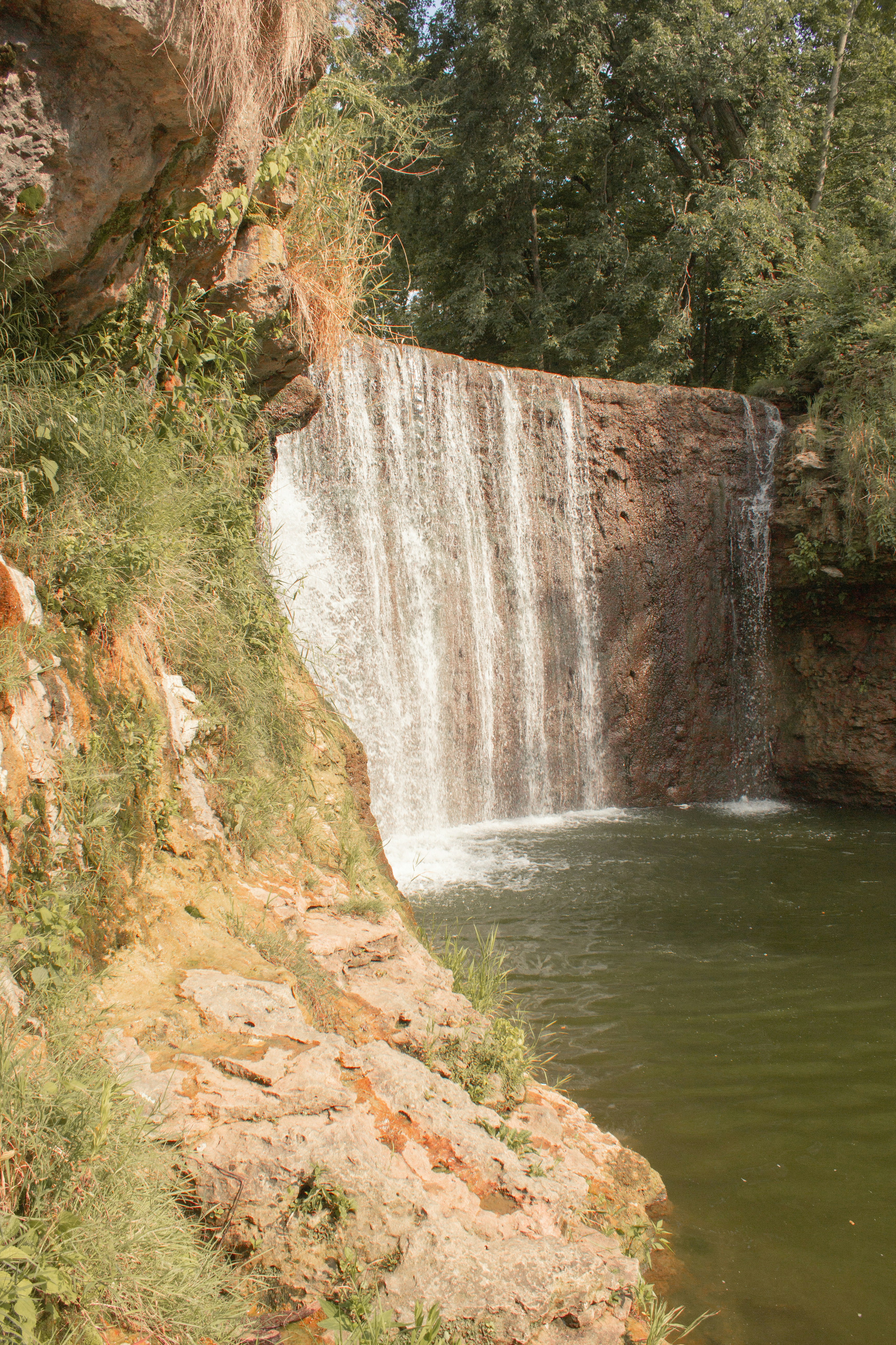 Waterfall cascading into a serene pool surrounded by lush greenery and rocky terrain.