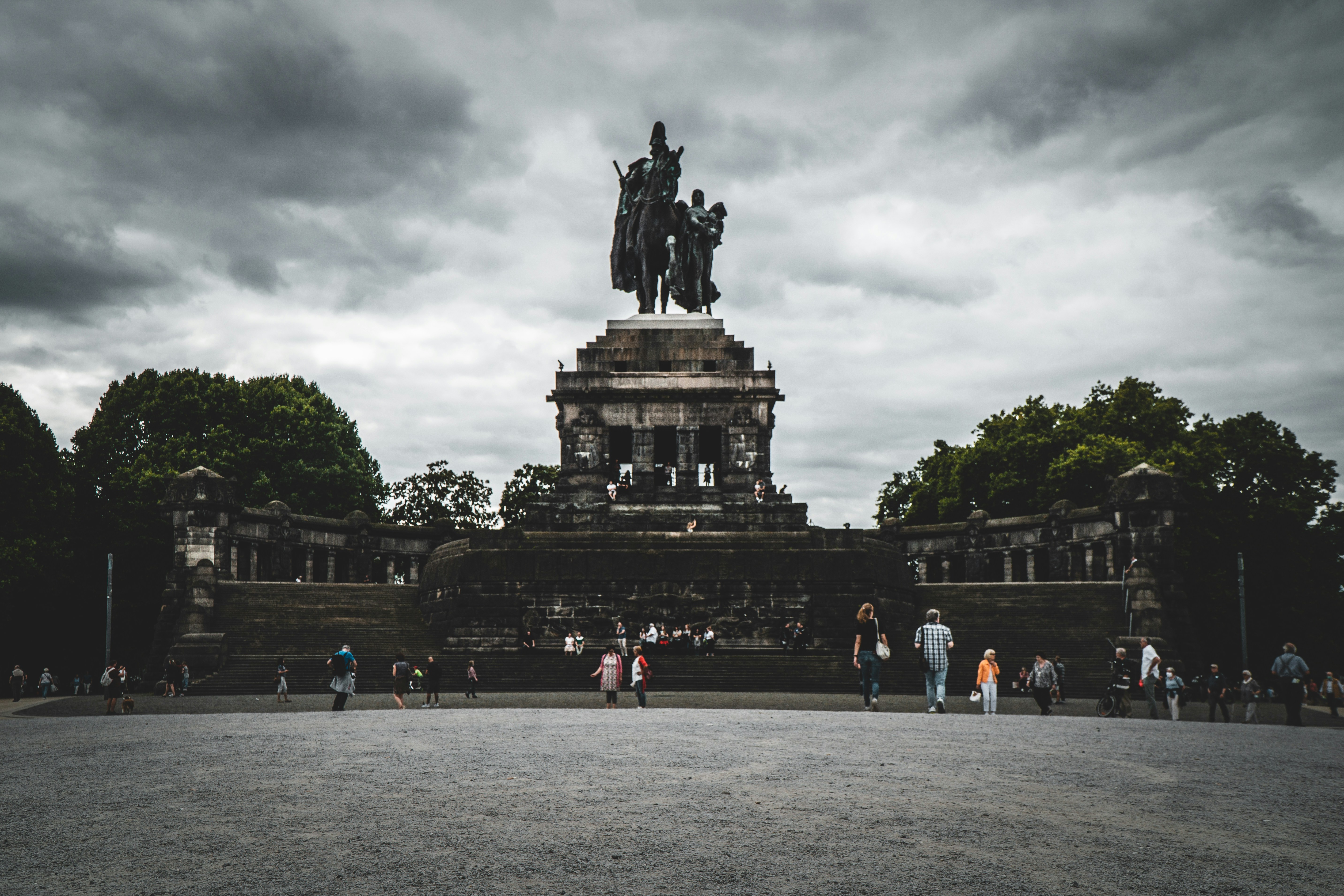 Monumental Statue and Sculptural Group Rising Over a Crowded Plaza