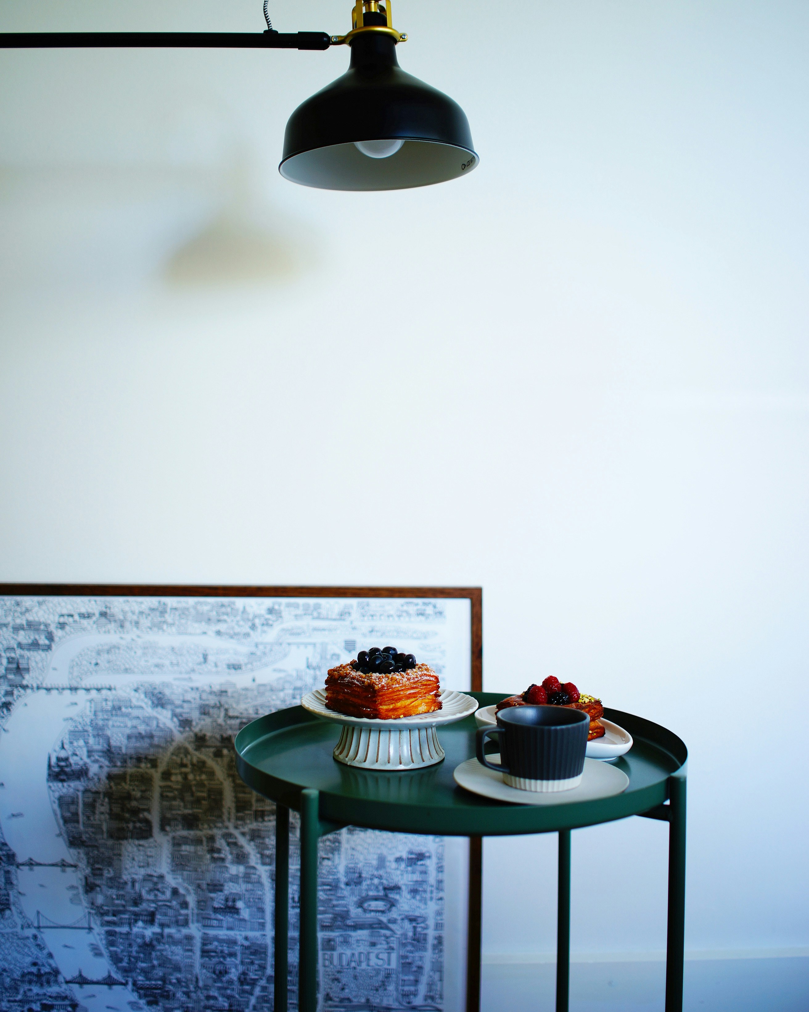 A stylish arrangement of pastries and coffee on a green table, complemented by a vintage map in the background. The scene evokes a cozy café atmosphere.