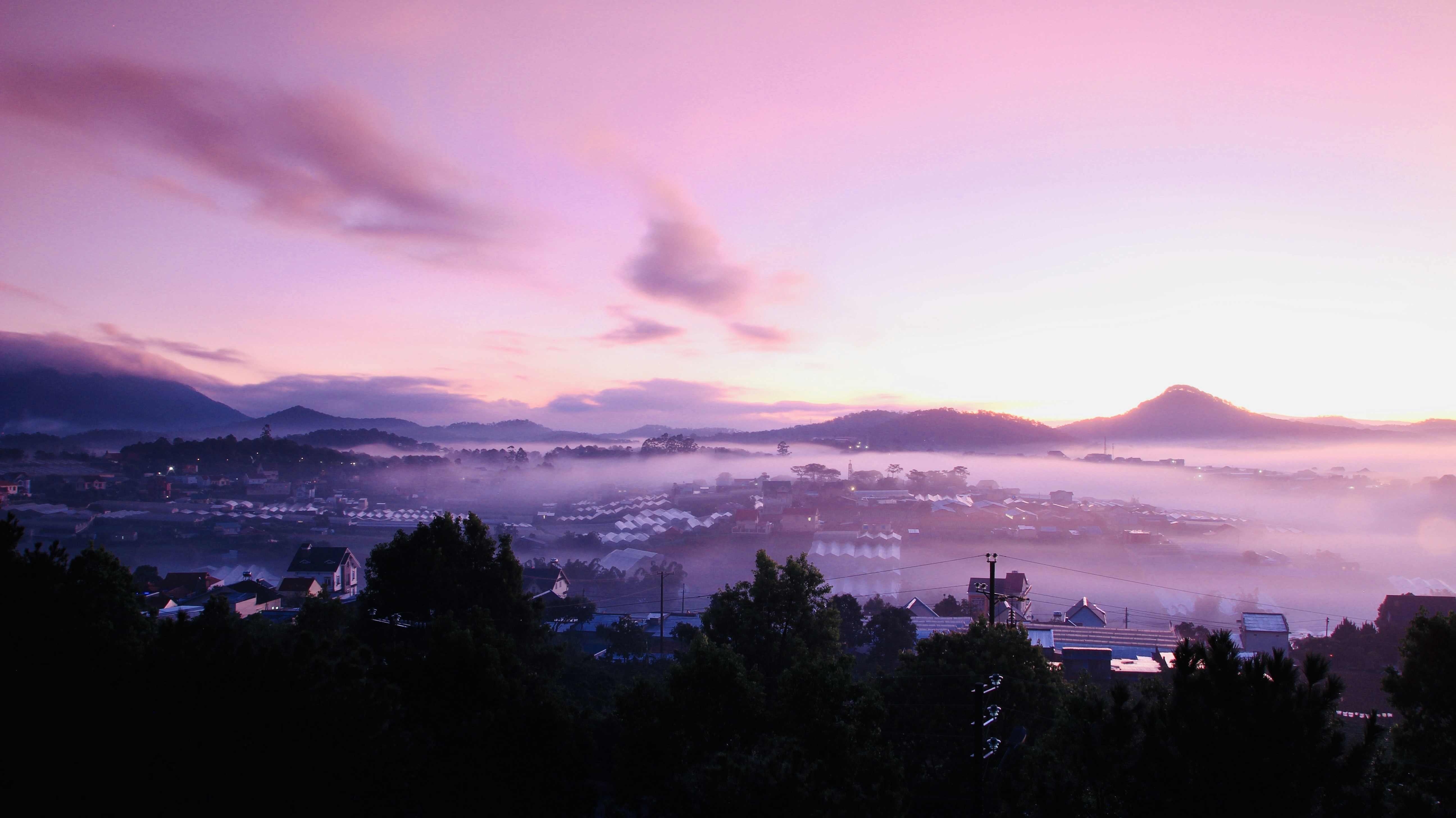 City skyline enveloped in morning mist with mountains silhouetted against a pastel sky.