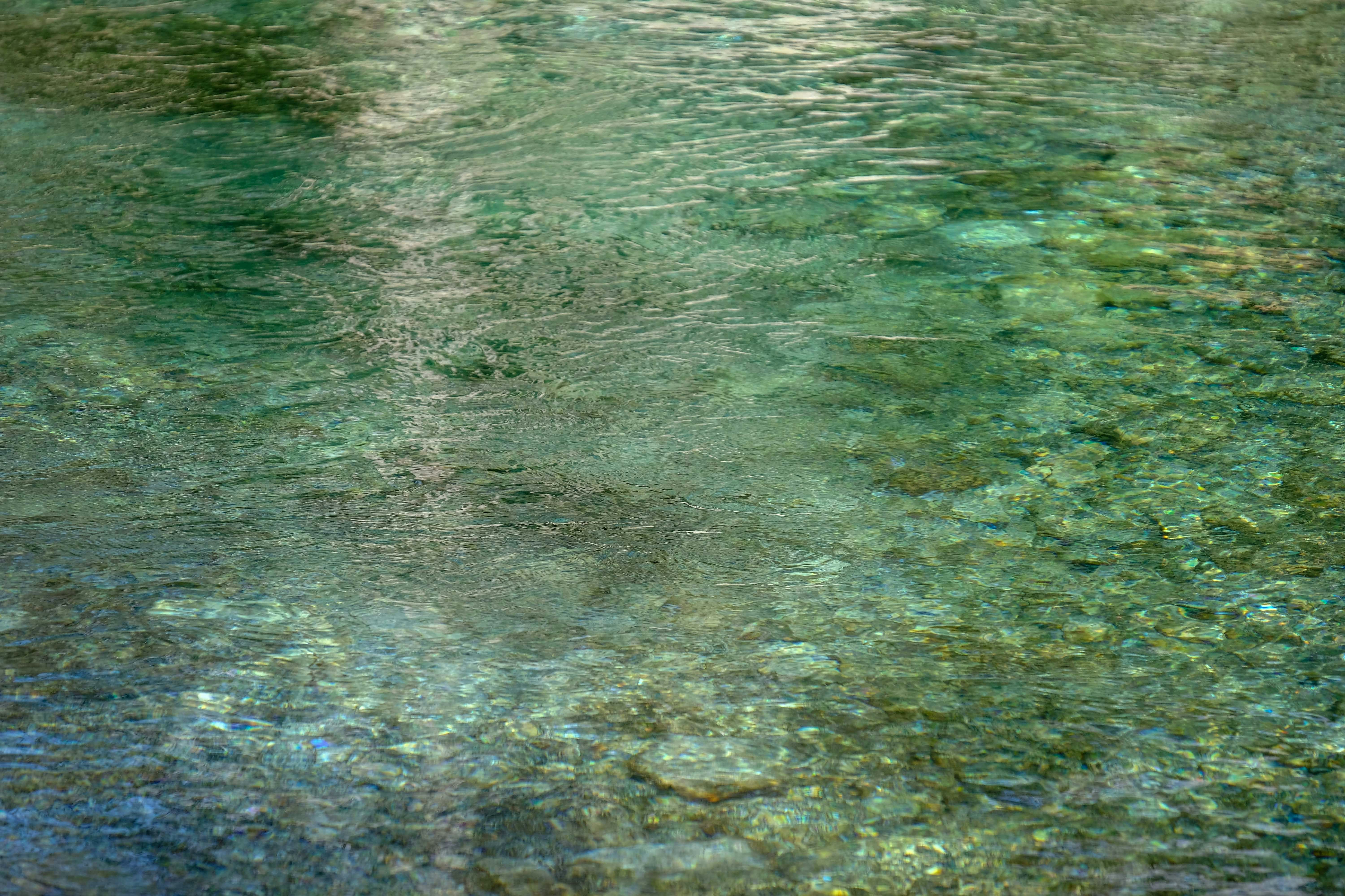 Crystal-clear water revealing colorful stones and gentle ripples, creating a serene aquatic landscape.