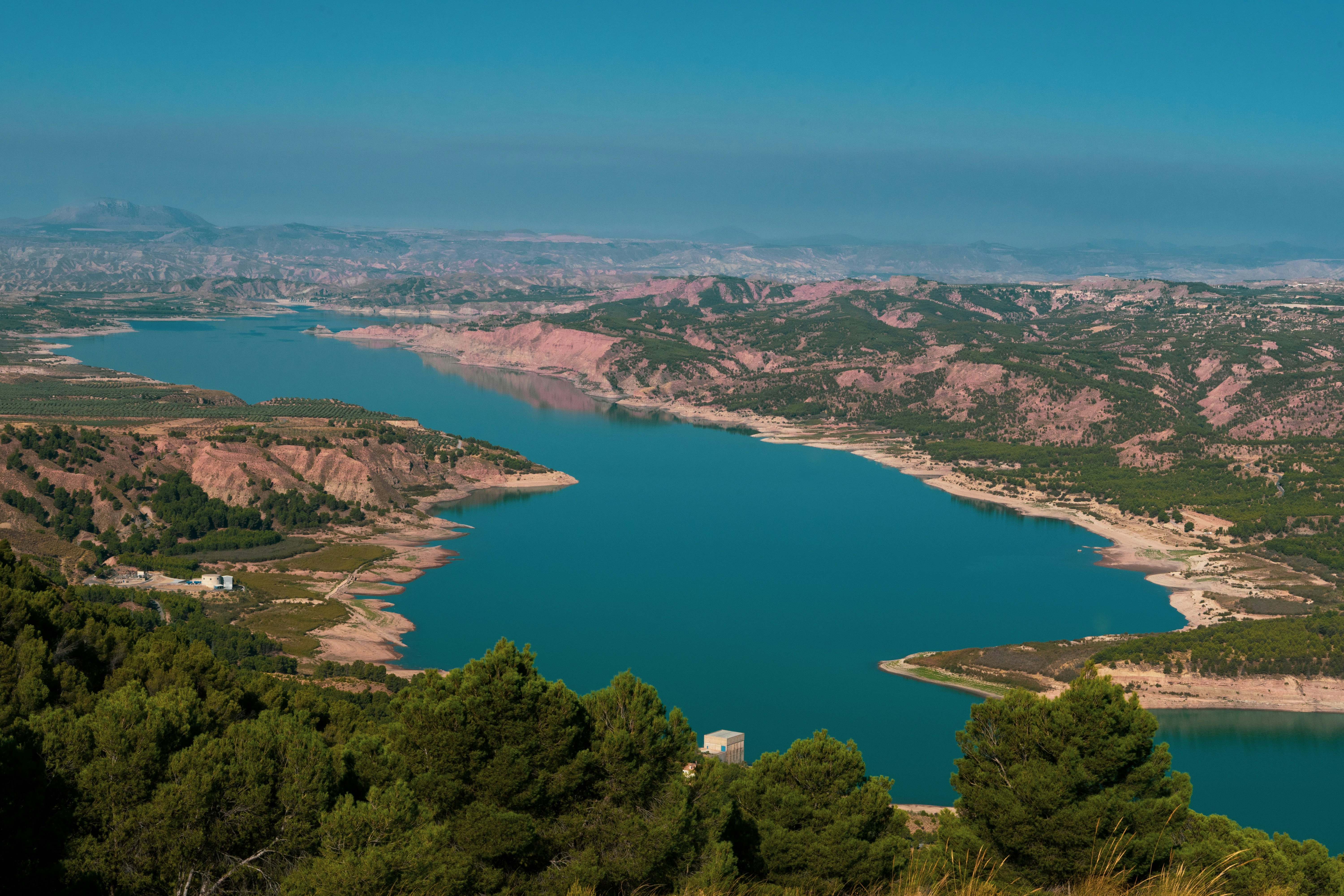 Expansive view of Negration Reservoir surrounded by lush vegetation and distant hills under a clear blue sky.