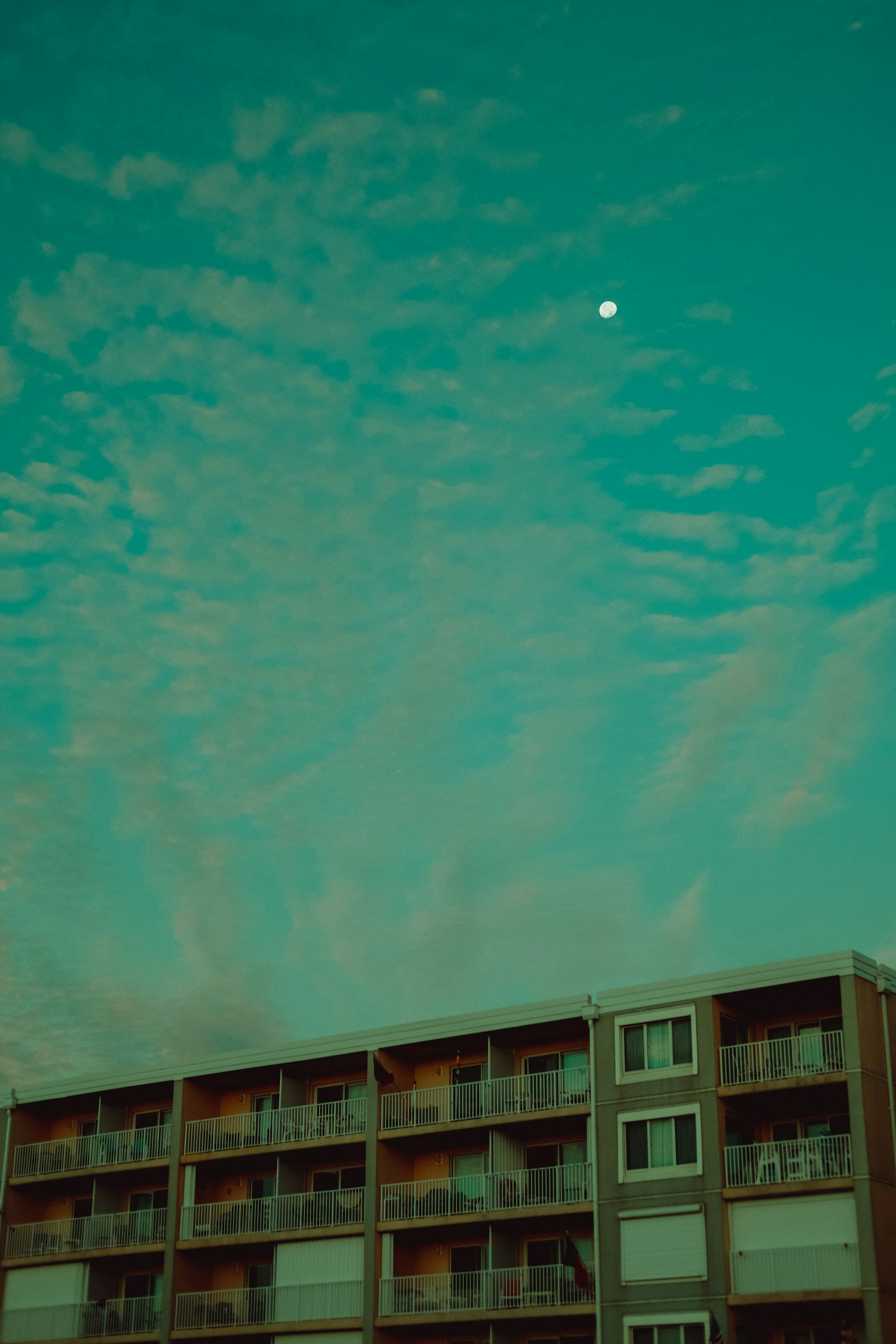 A tranquil evening scene featuring a residential building under a textured sky with a bright moon. The colors evoke a serene atmosphere.