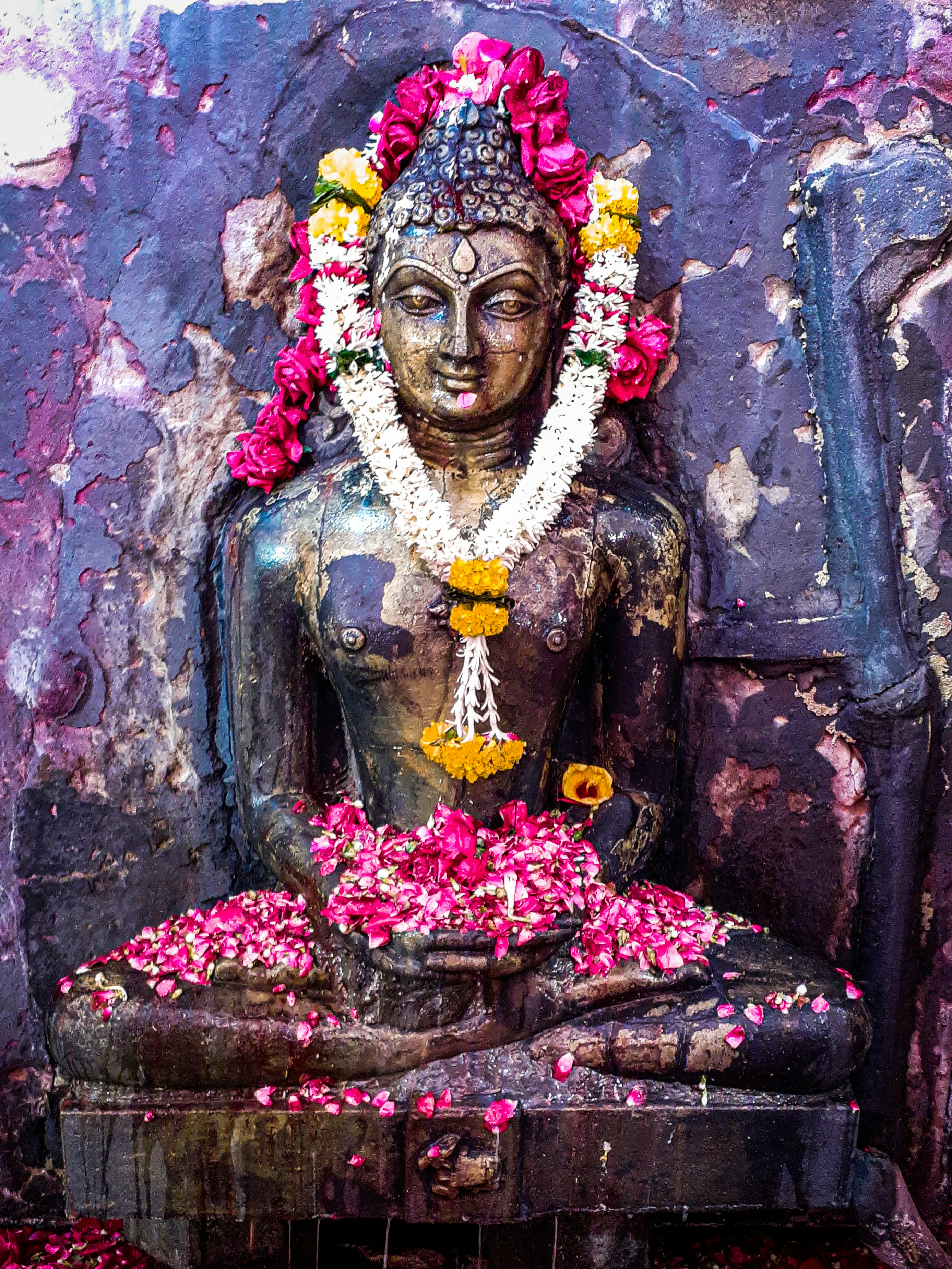 Ancient seated Buddha statue adorned with vibrant flower garlands and petals.