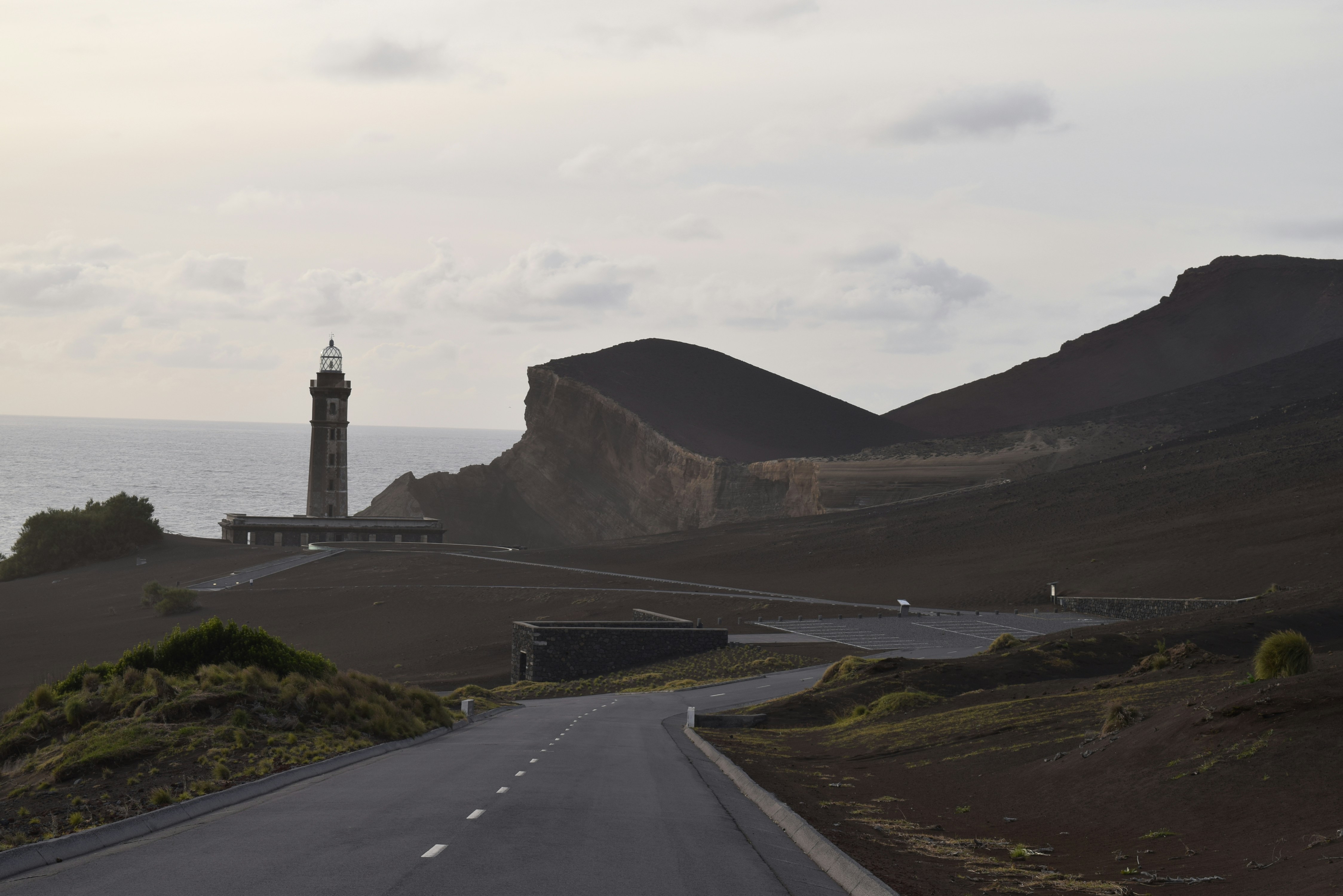 A solitary lighthouse stands tall against a backdrop of dark volcanic terrain and a serene ocean, highlighting the contrast between nature and human ingenuity.