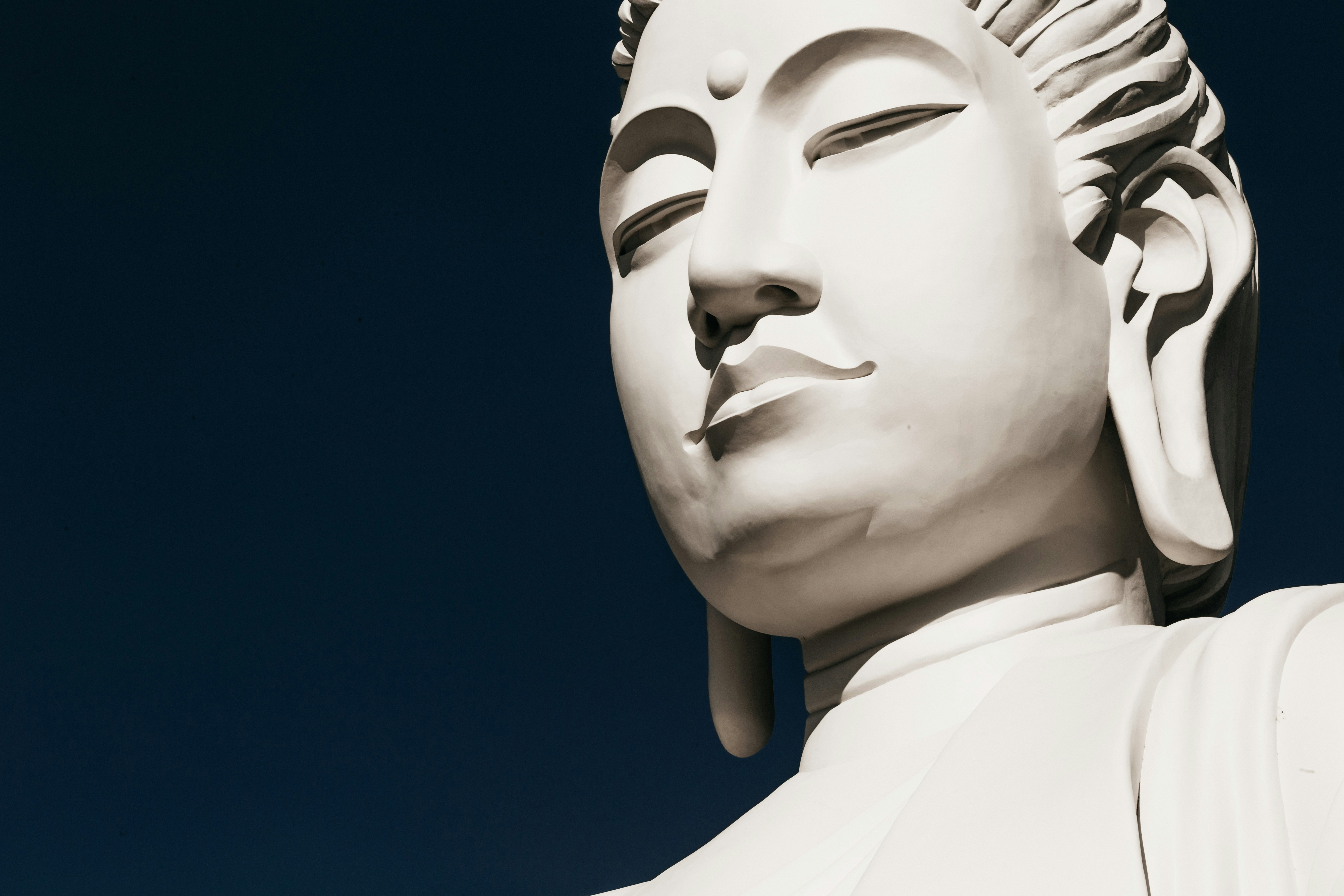Close-up of a white stone Buddha statue with serene expression under a clear blue sky.