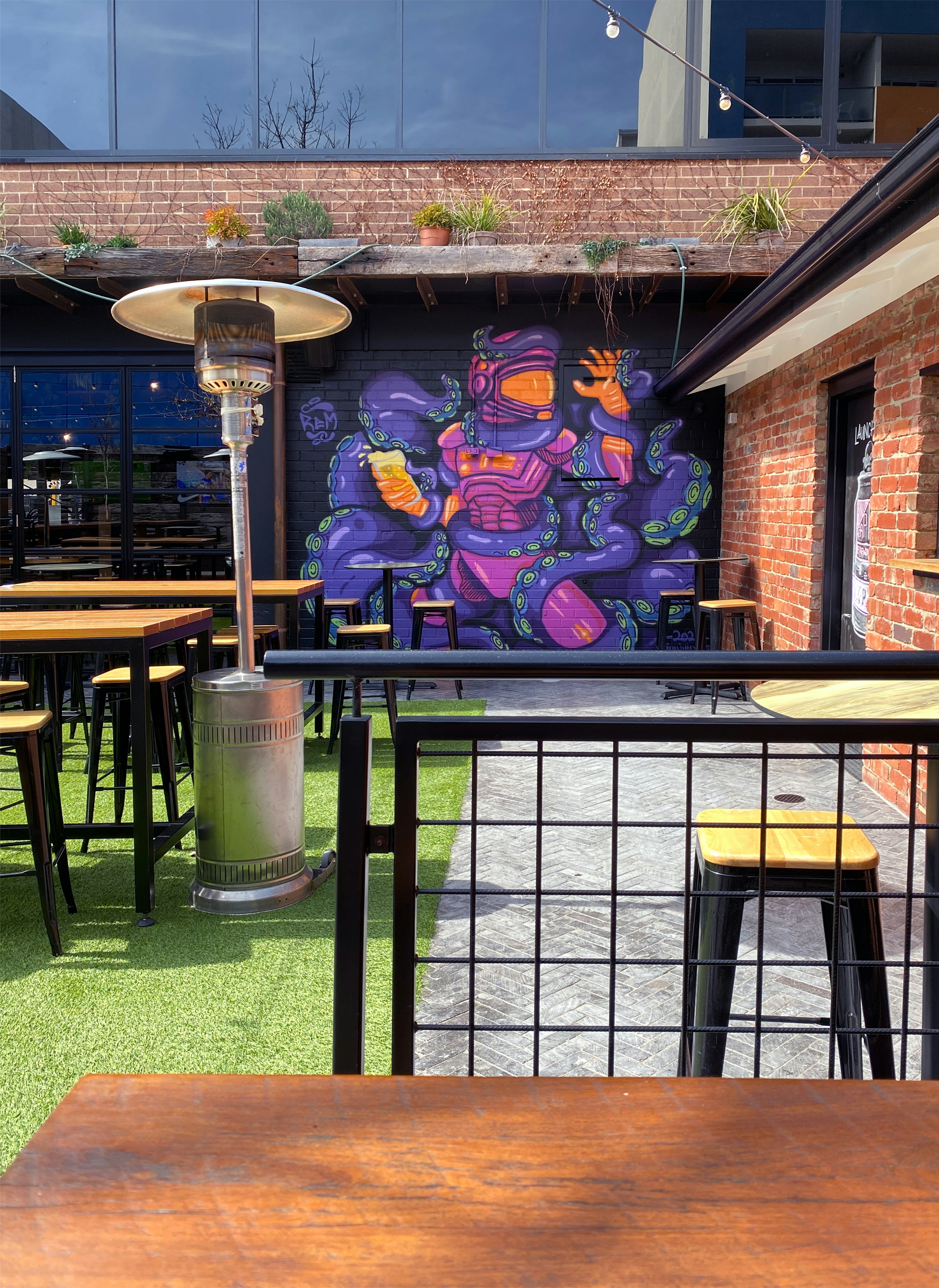 Vibrant mural of a cosmic figure surrounded by tentacles, set against a rustic brick backdrop in an outdoor dining area.