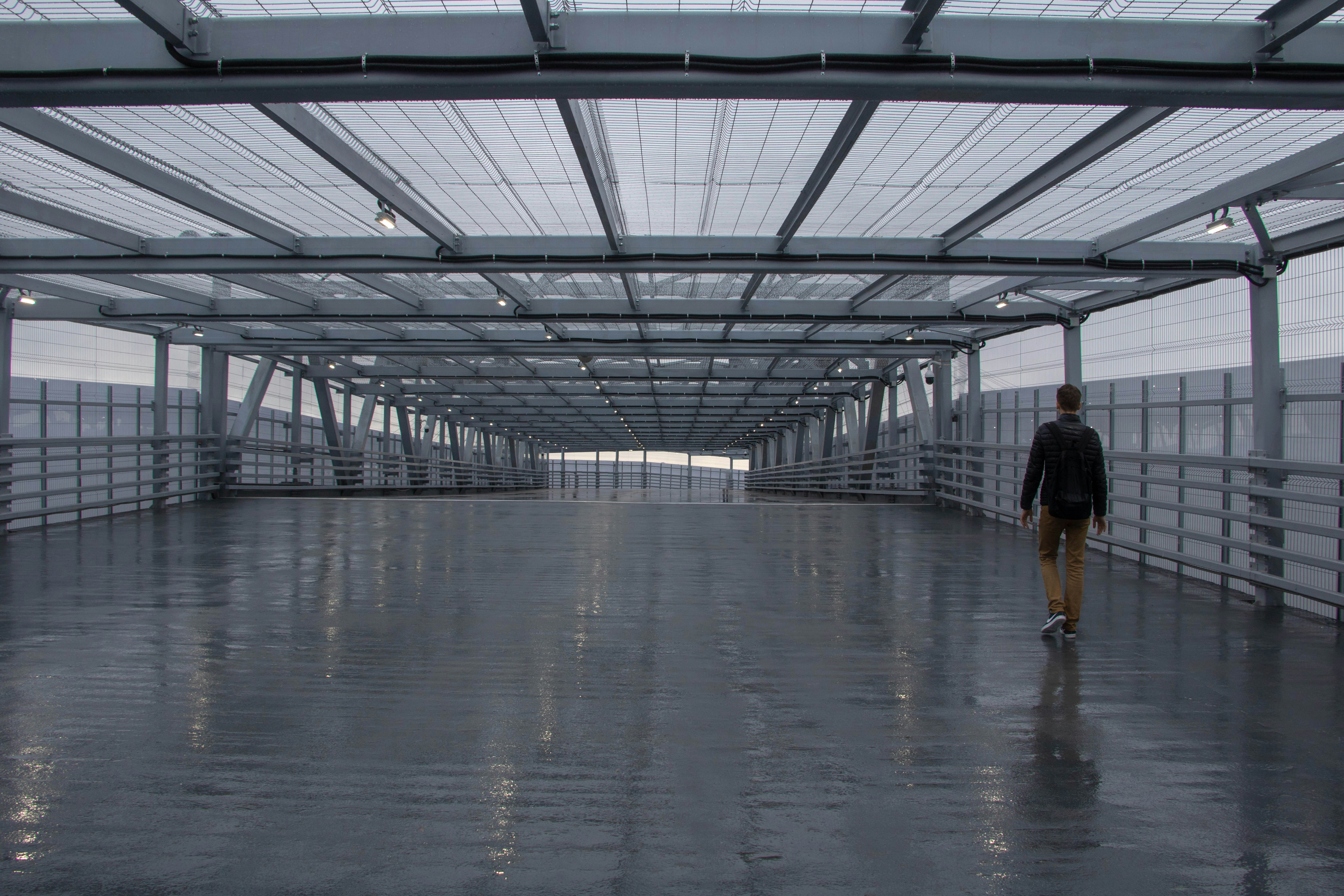 A solitary figure walks across a vast, reflective surface beneath a transparent roof, evoking a sense of tranquility and isolation.