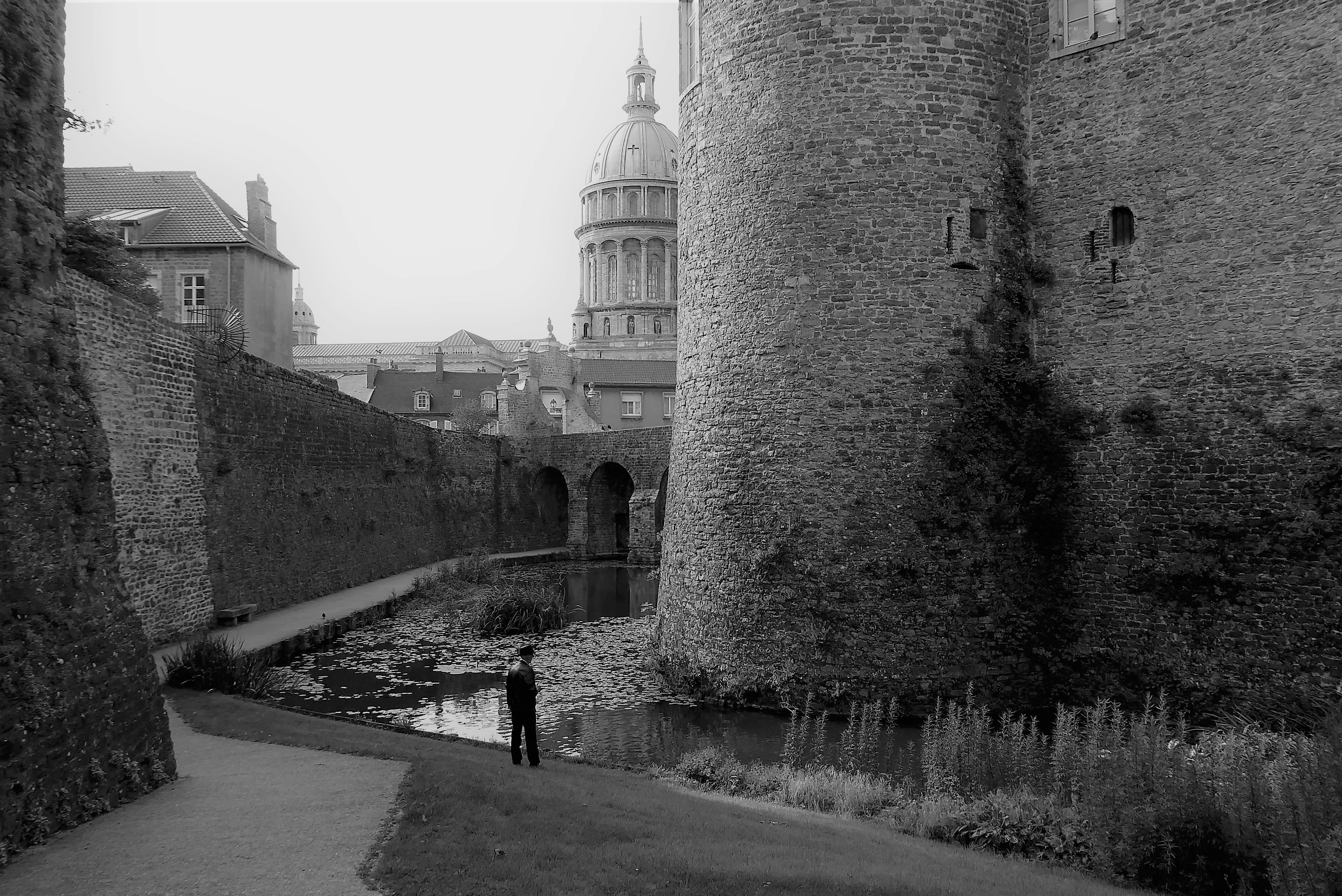 Grayscale view of ancient stone walls with a domed building in the background.