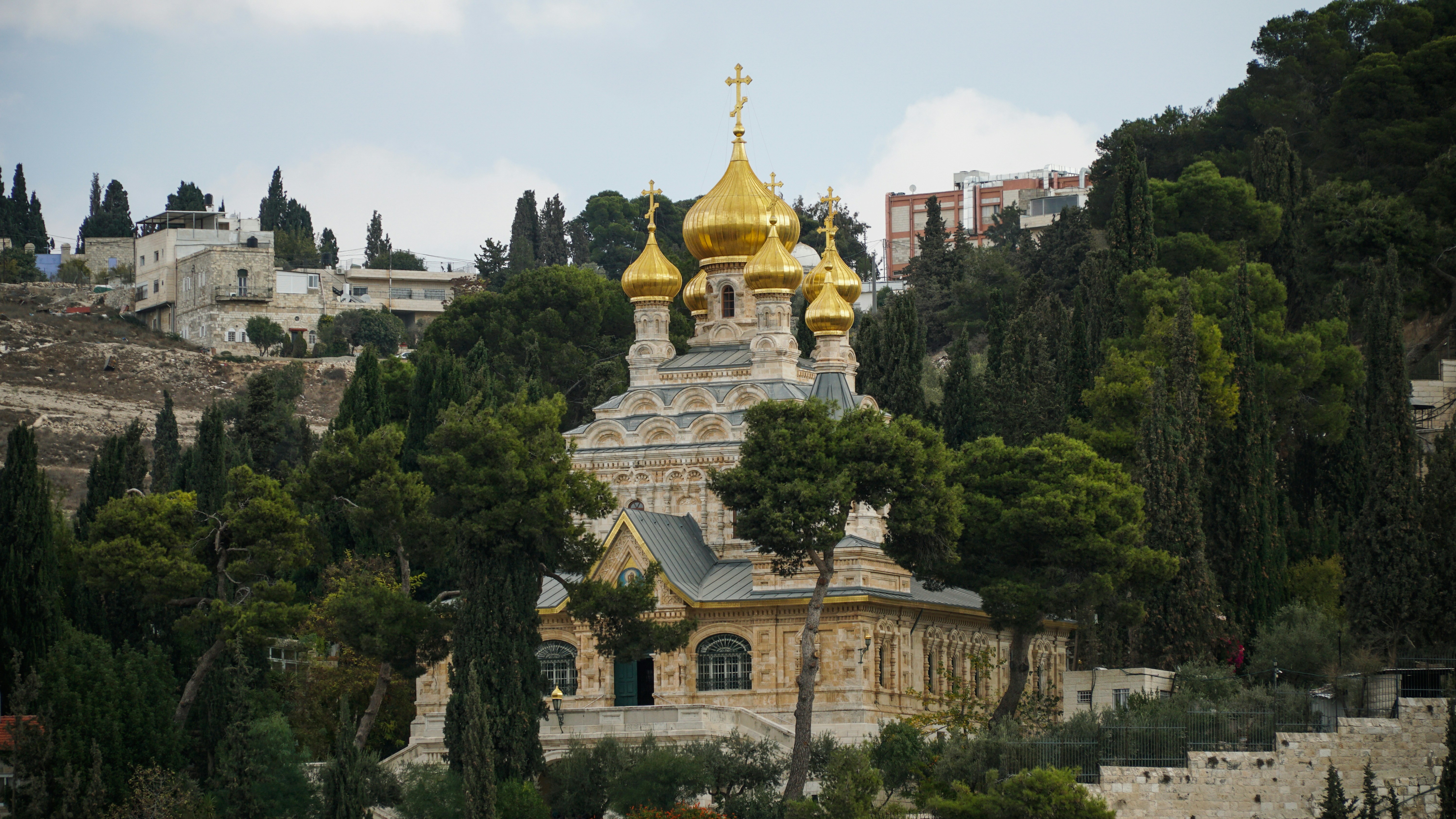 Historic church with golden domes nestled among lush pine trees on a hillside.