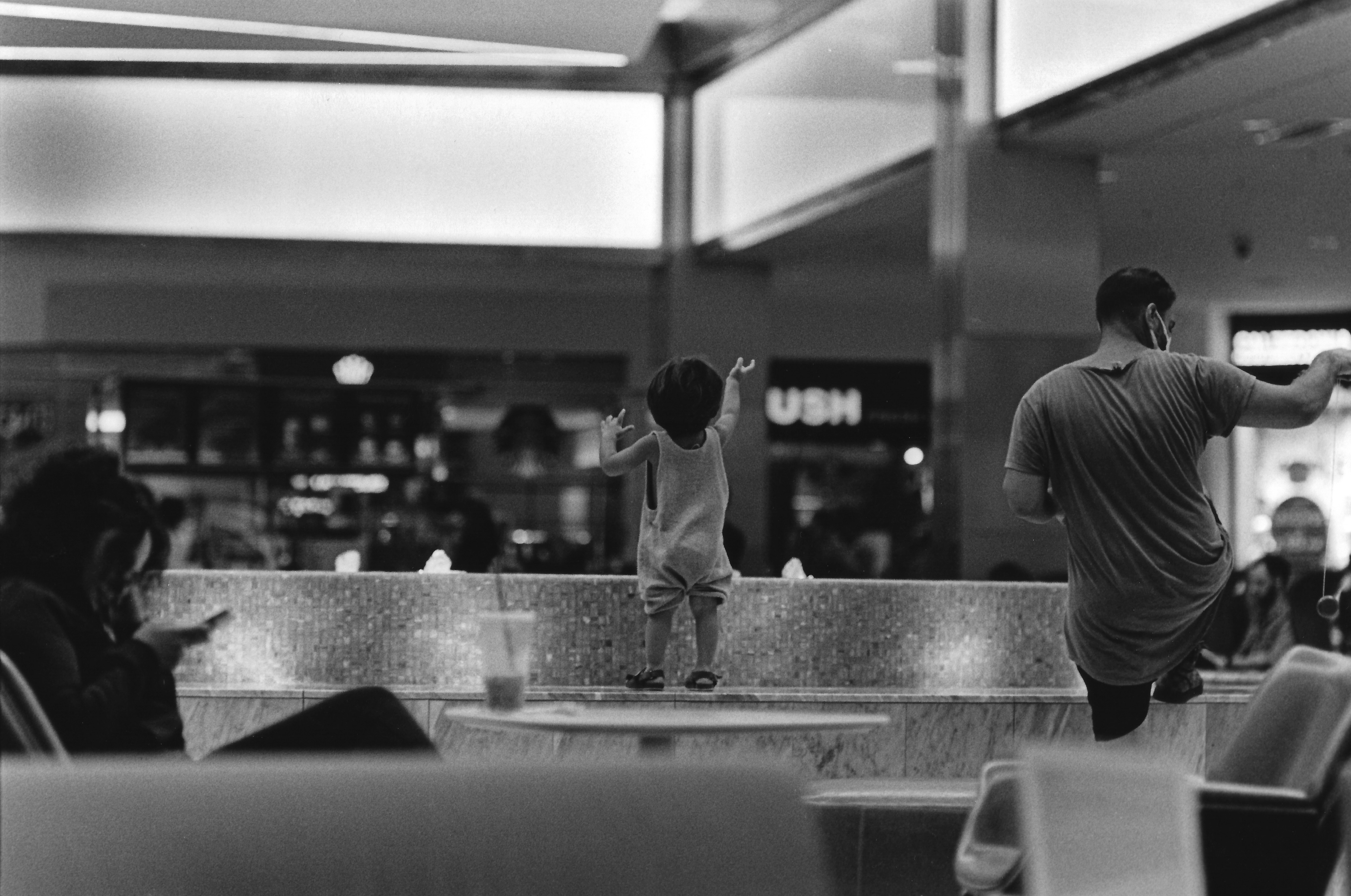 Child standing on a counter in a busy indoor setting with adults nearby.