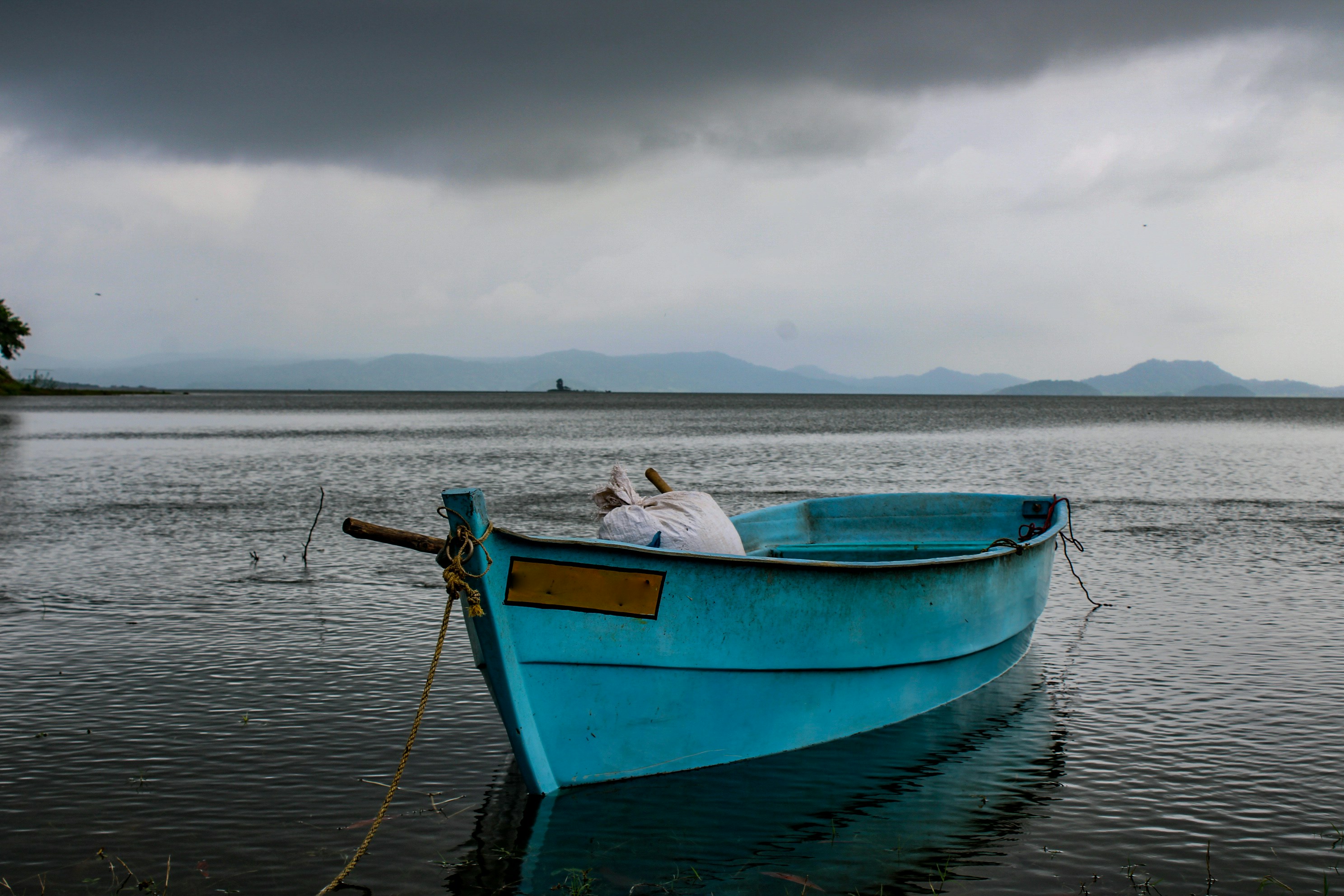 Azure rowboat afloat at harbor under brooding clouds