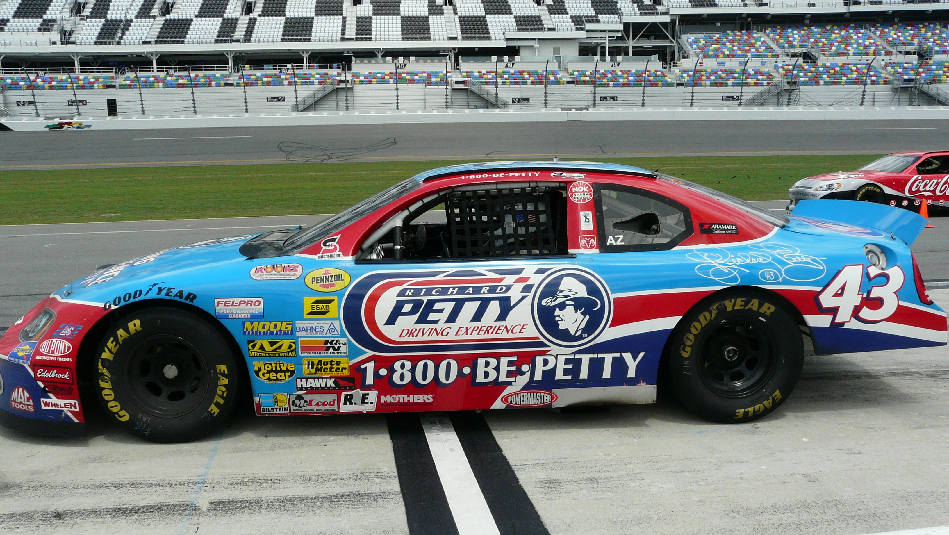 Red, white, and blue race car with sponsorship logos parked on a racetrack.