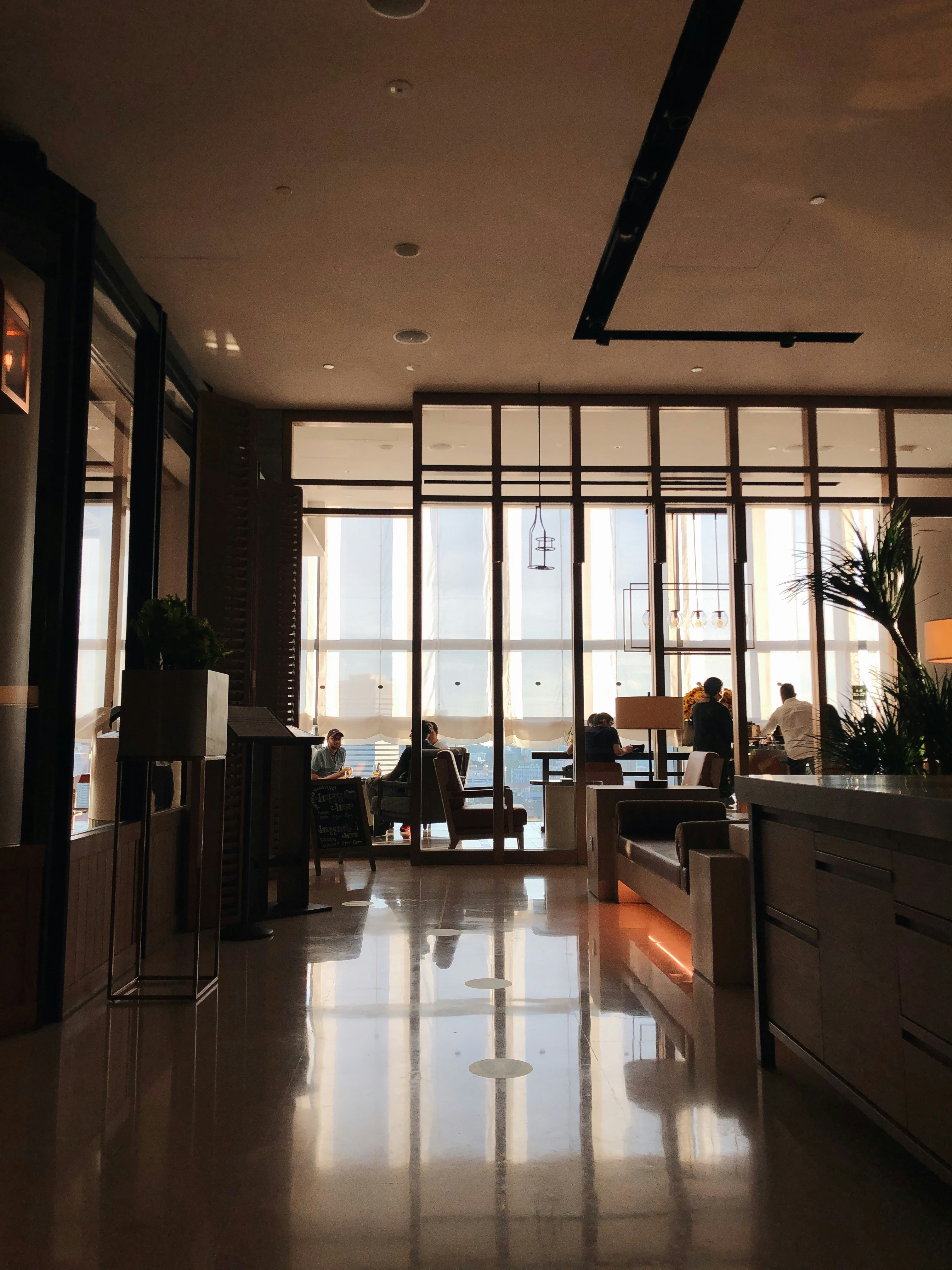 Contemporary interior of a stylish café with large windows offering a view of the city skyline. Patrons enjoy their time in a well-lit, modern space.