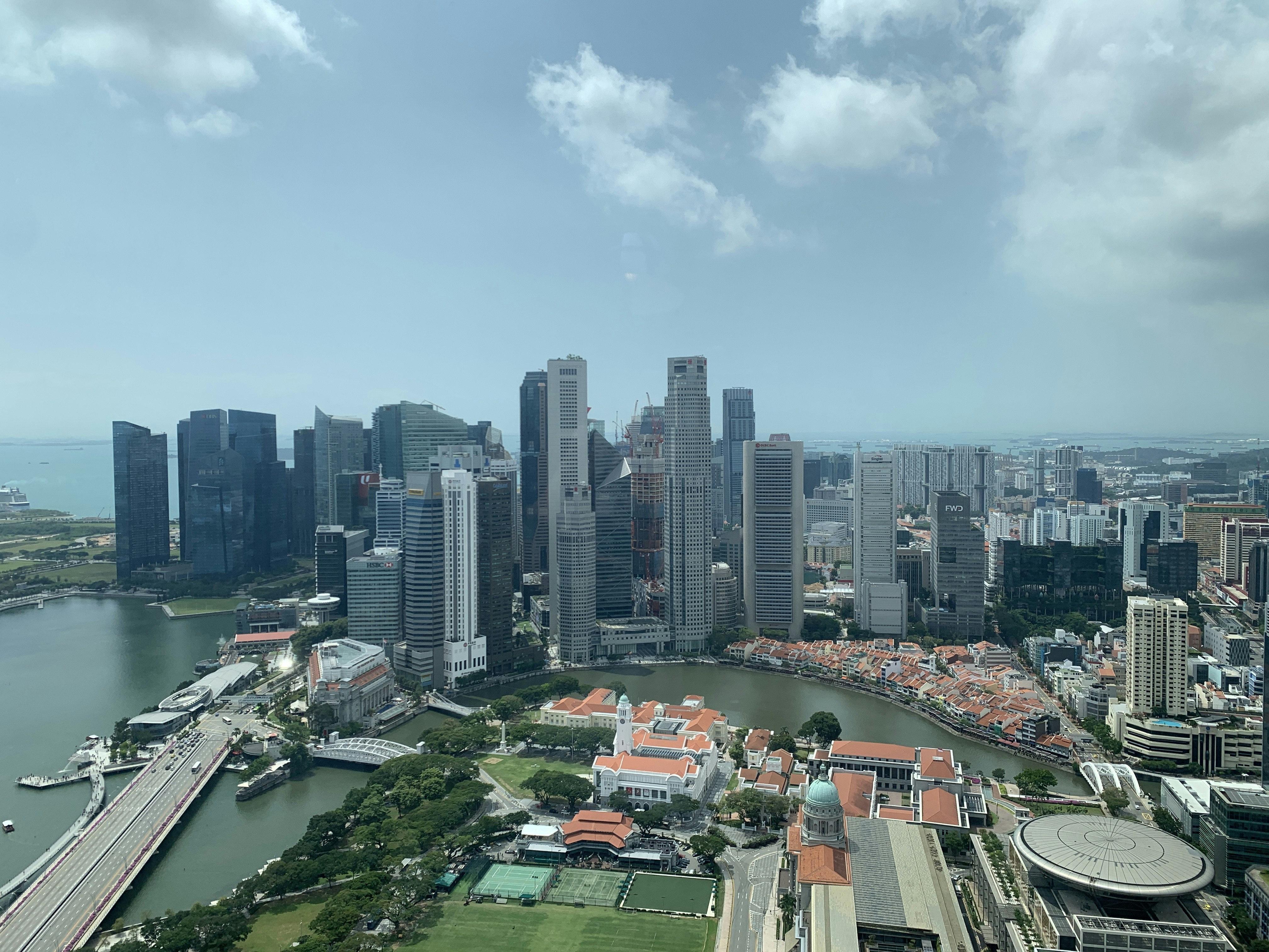 Aerial view of Singapore's skyline showcasing a blend of modern skyscrapers and lush greenery along the waterfront. The scene captures the city's vibrant urban landscape.