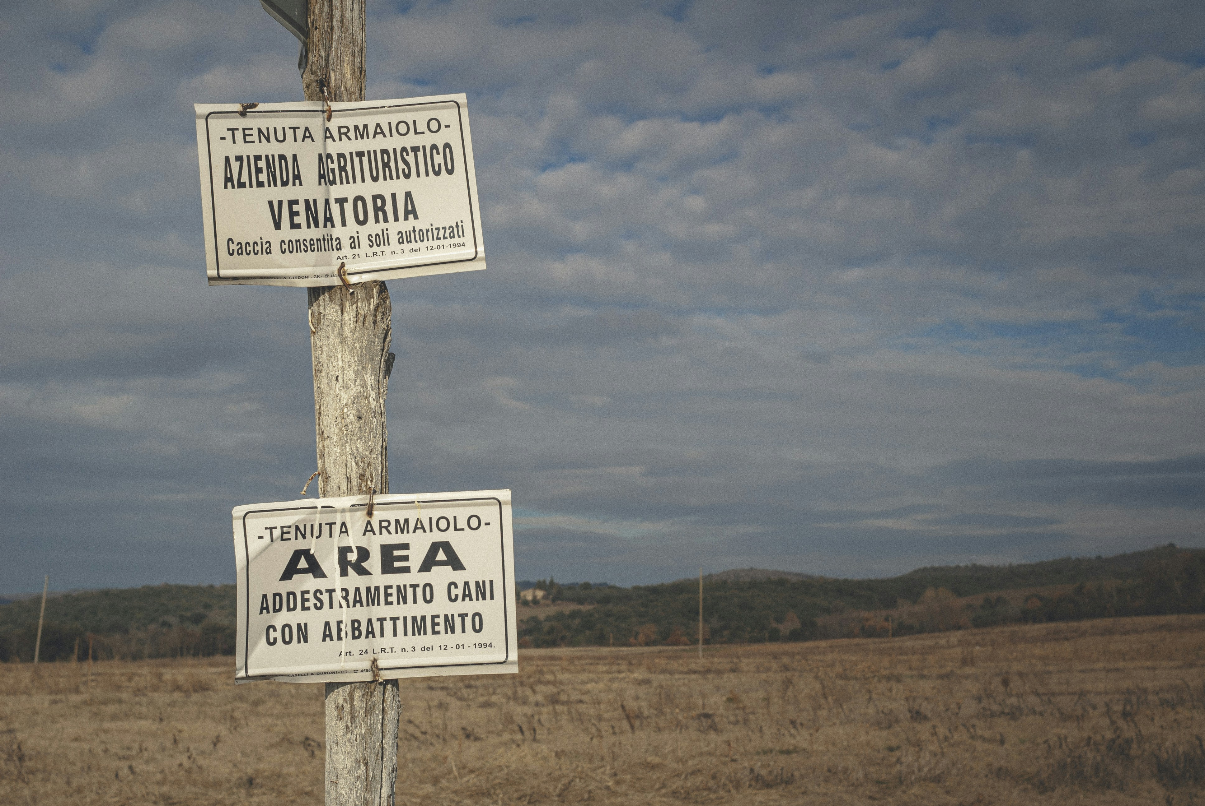 Two weathered signs mounted on a wooden post, indicating an agritourism venue and a dog training area in a rural landscape.