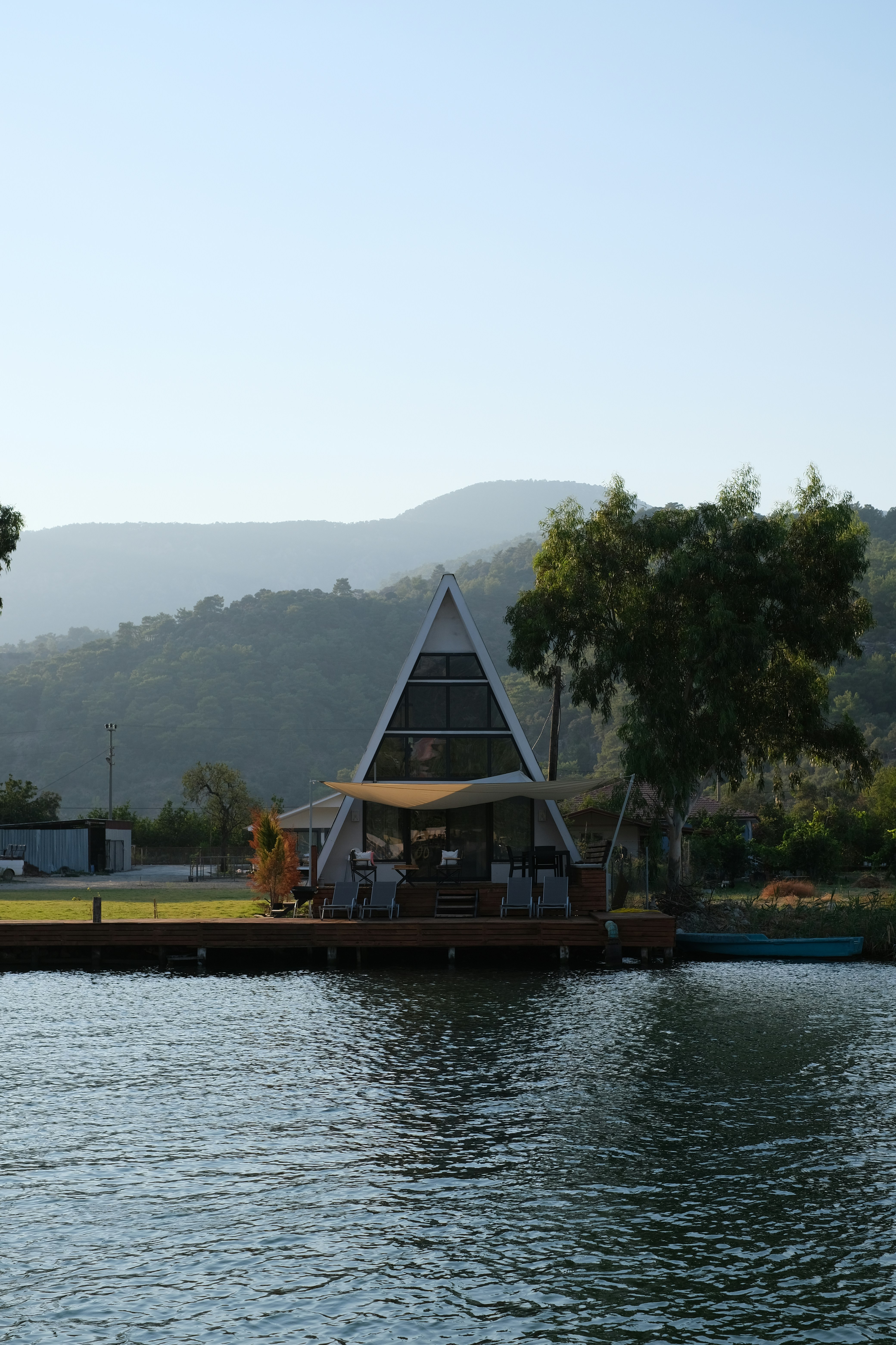 Cozy brown wooden cabin nestled among green trees near a calm body of water, captured during daytime. Serene nature setting perfect for themes of retreat, cabin life, travel, tranquility, and sustainable living.
