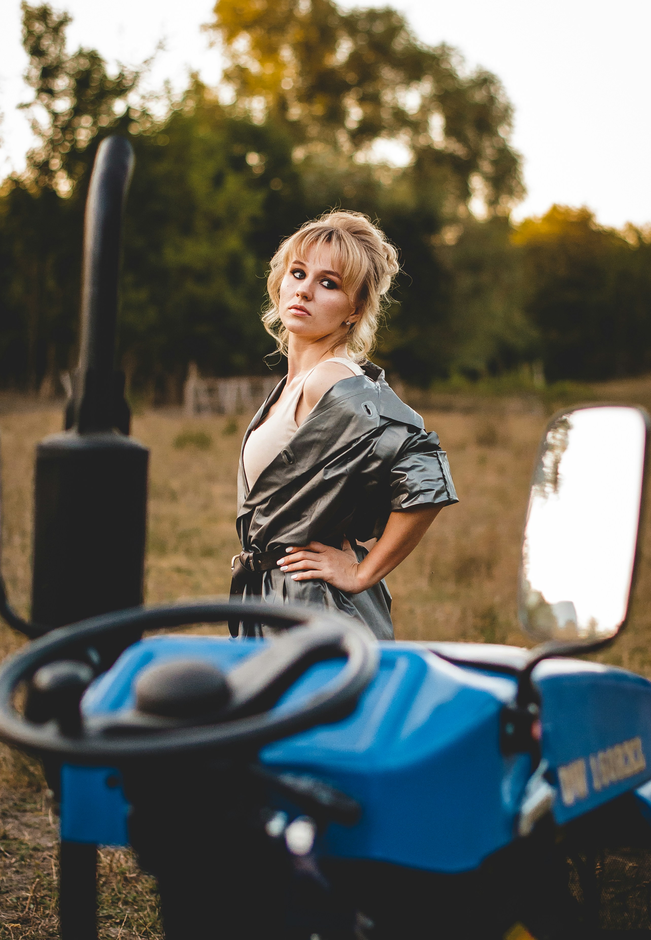Amber Hour Portrait: A Woman Beside a Blue Tractor in a Sunlit Field