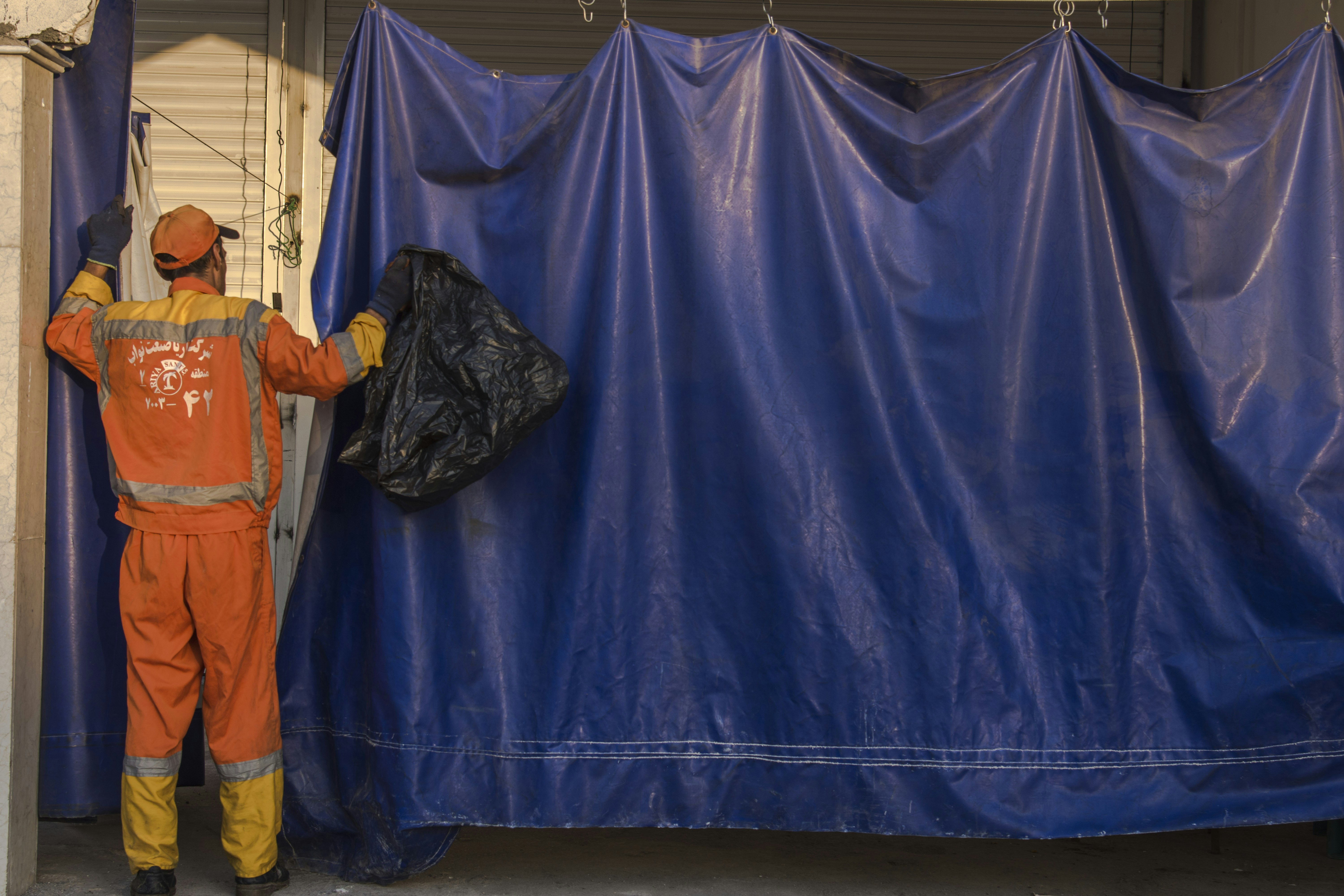 Securing the Blue Barrier: Two Orange-Clad Workers at a Jobsite Curtain