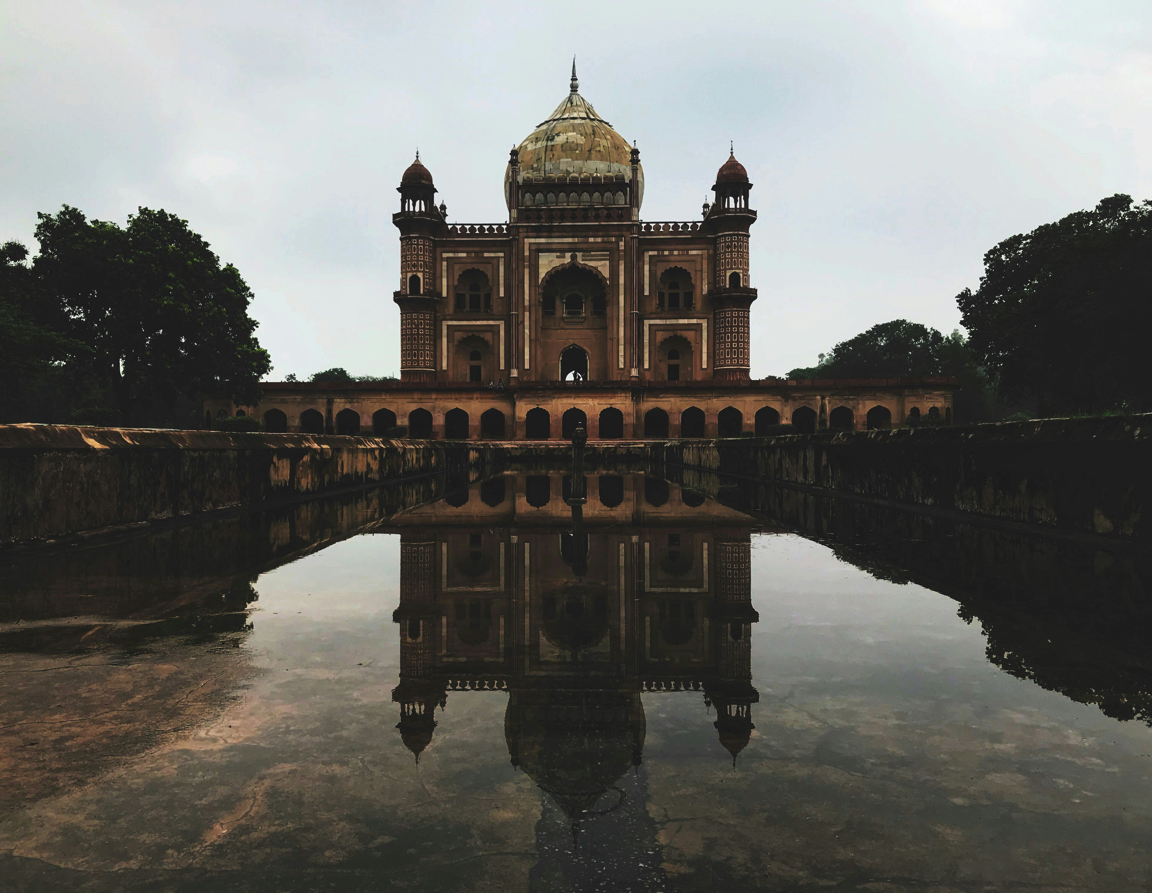 Historic mausoleum reflected in still water under a cloudy sky.