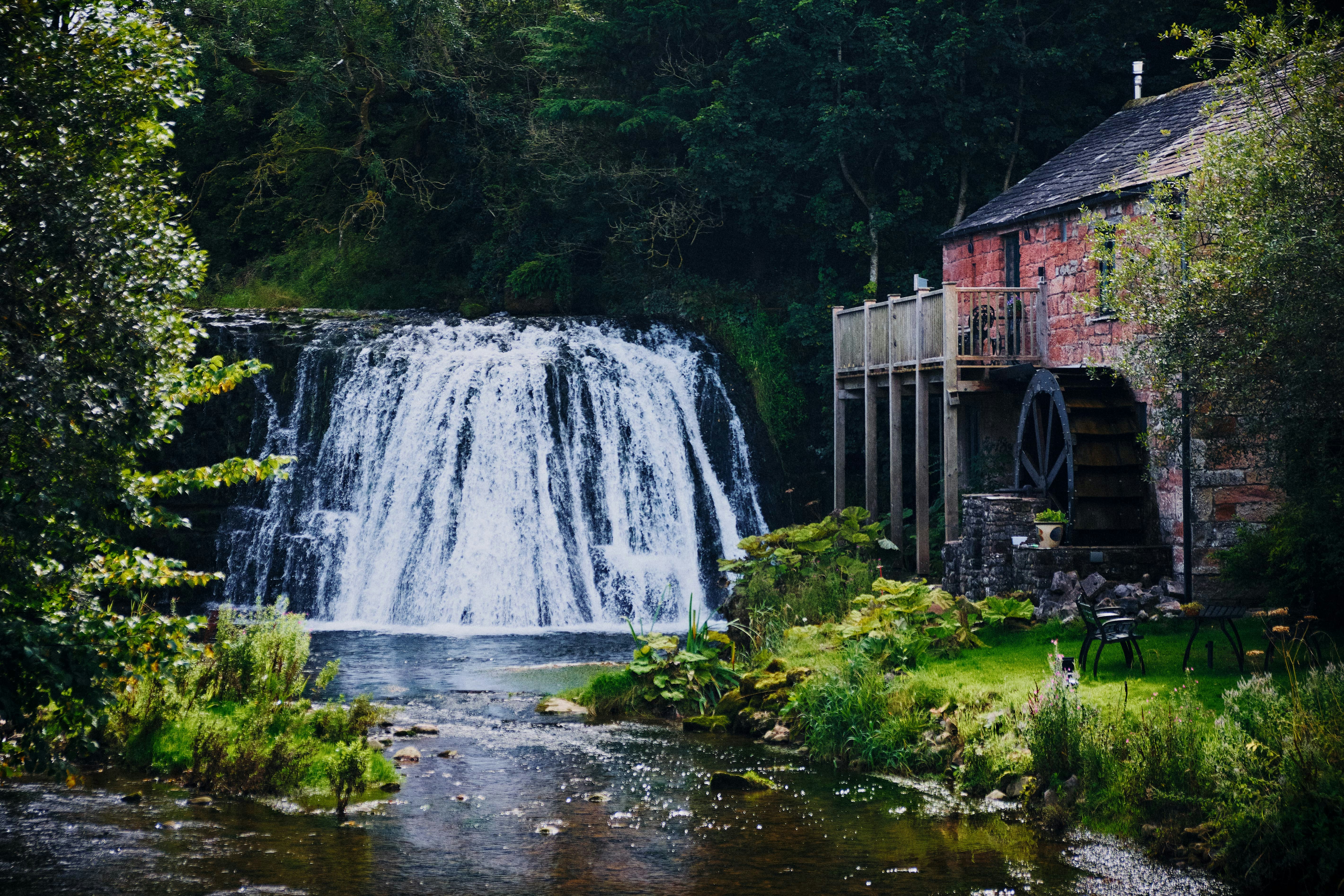 Waterfall cascading beside an old mill surrounded by lush greenery.