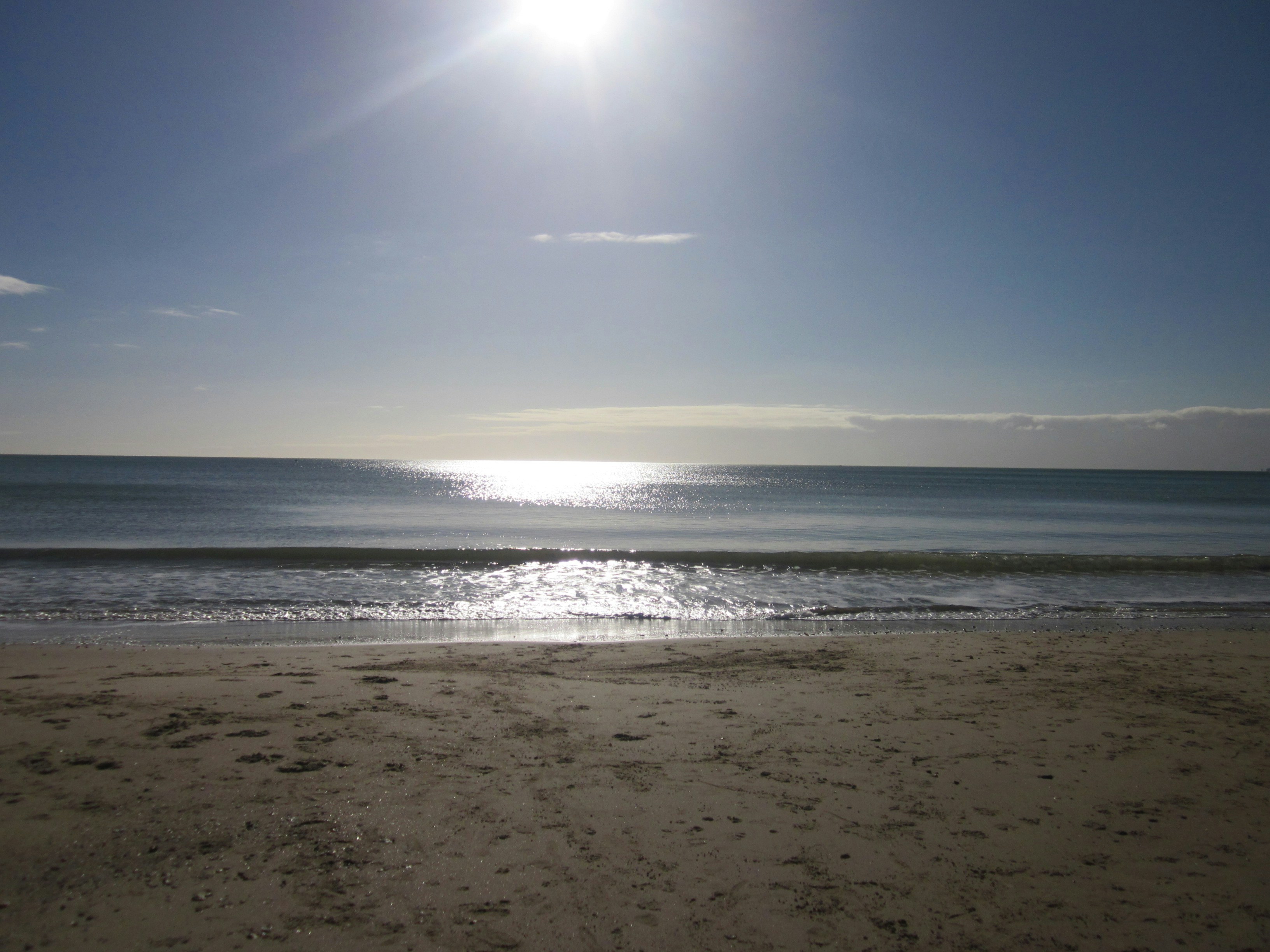 Glistening ocean waves gently lapping against a sandy beach under a bright sunlit sky.
