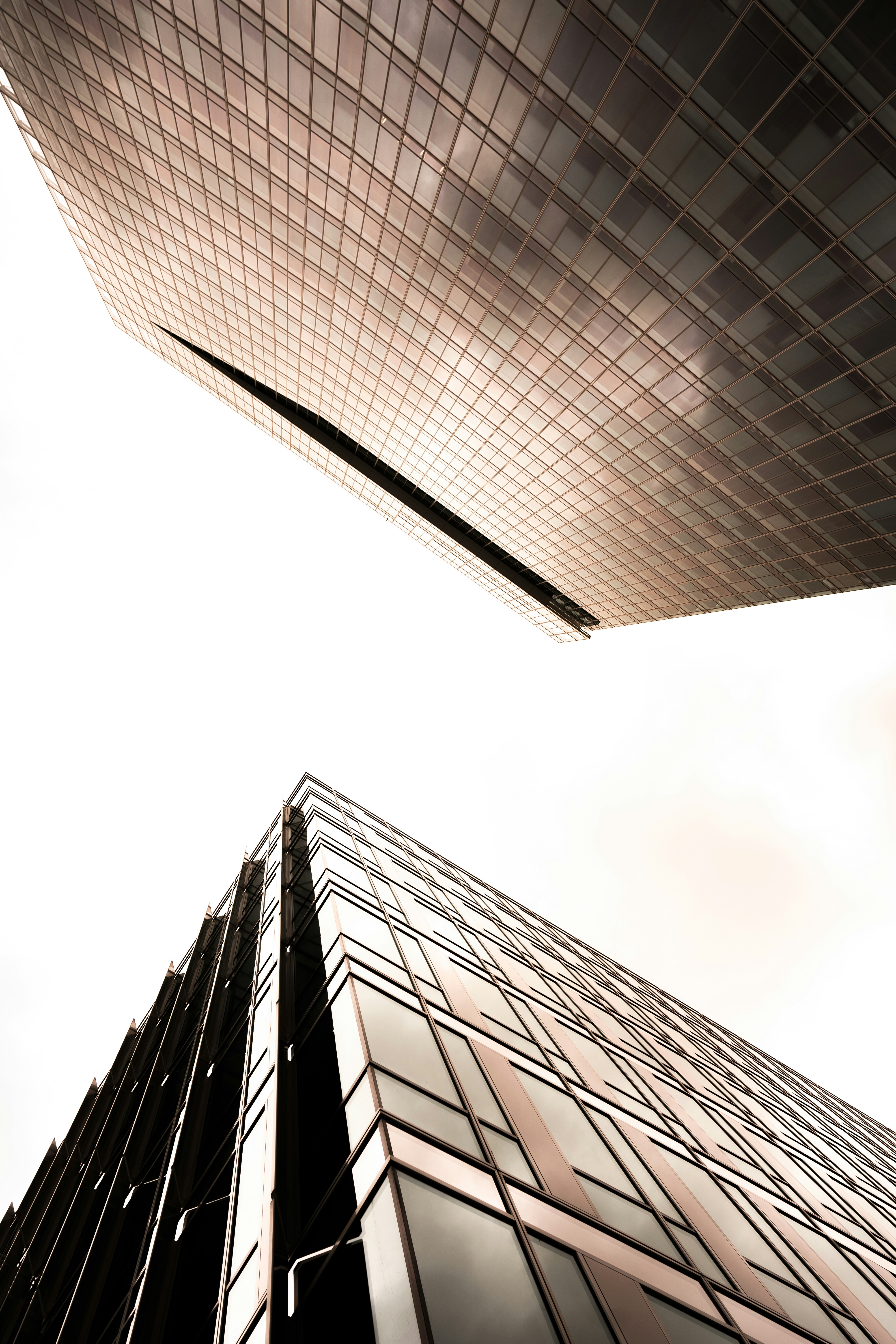 Two towering skyscrapers captured from a low angle, showcasing their reflective surfaces against a bright sky.