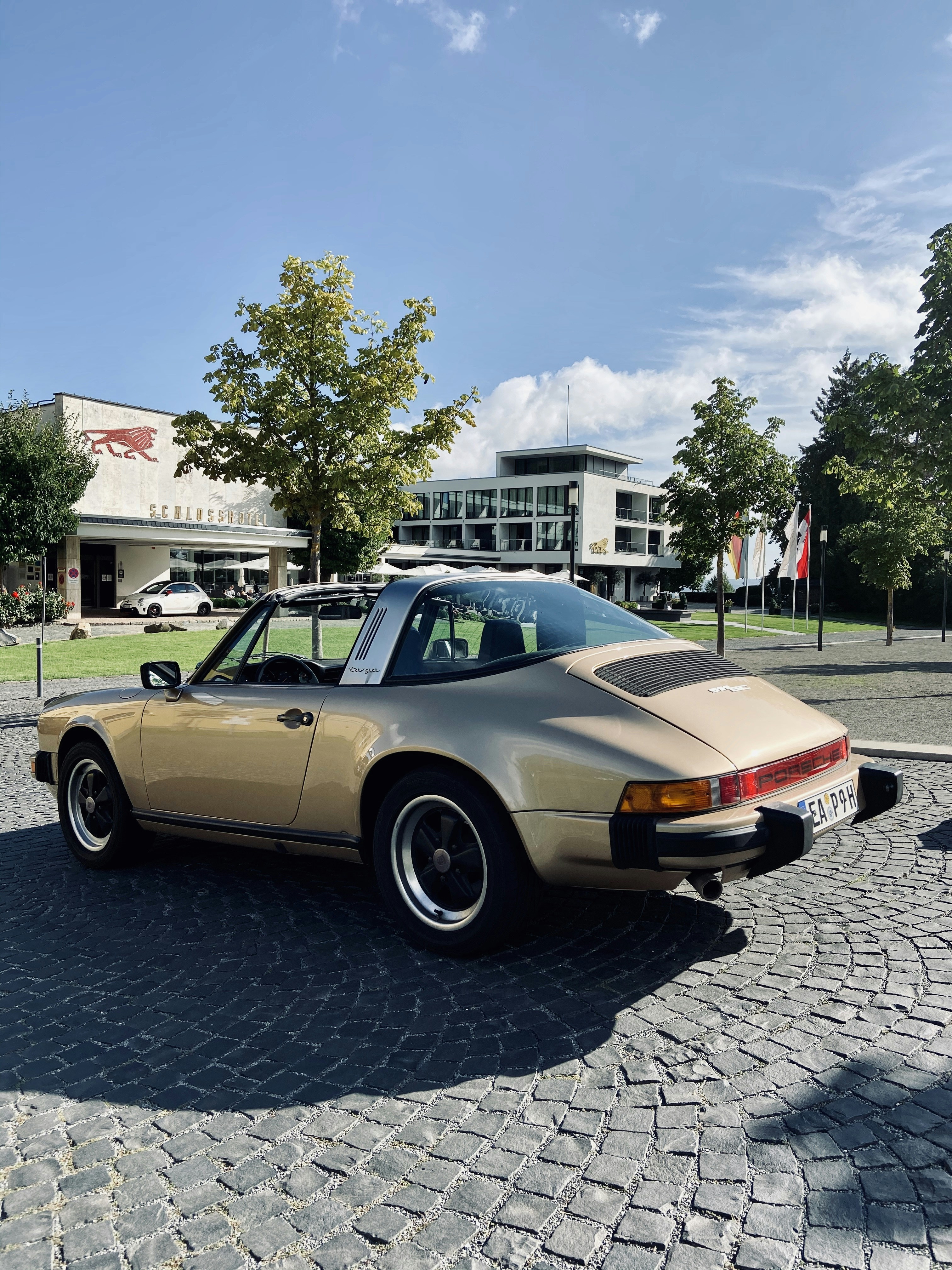 Vintage gold sports car parked on cobblestone street with modern buildings in the background.