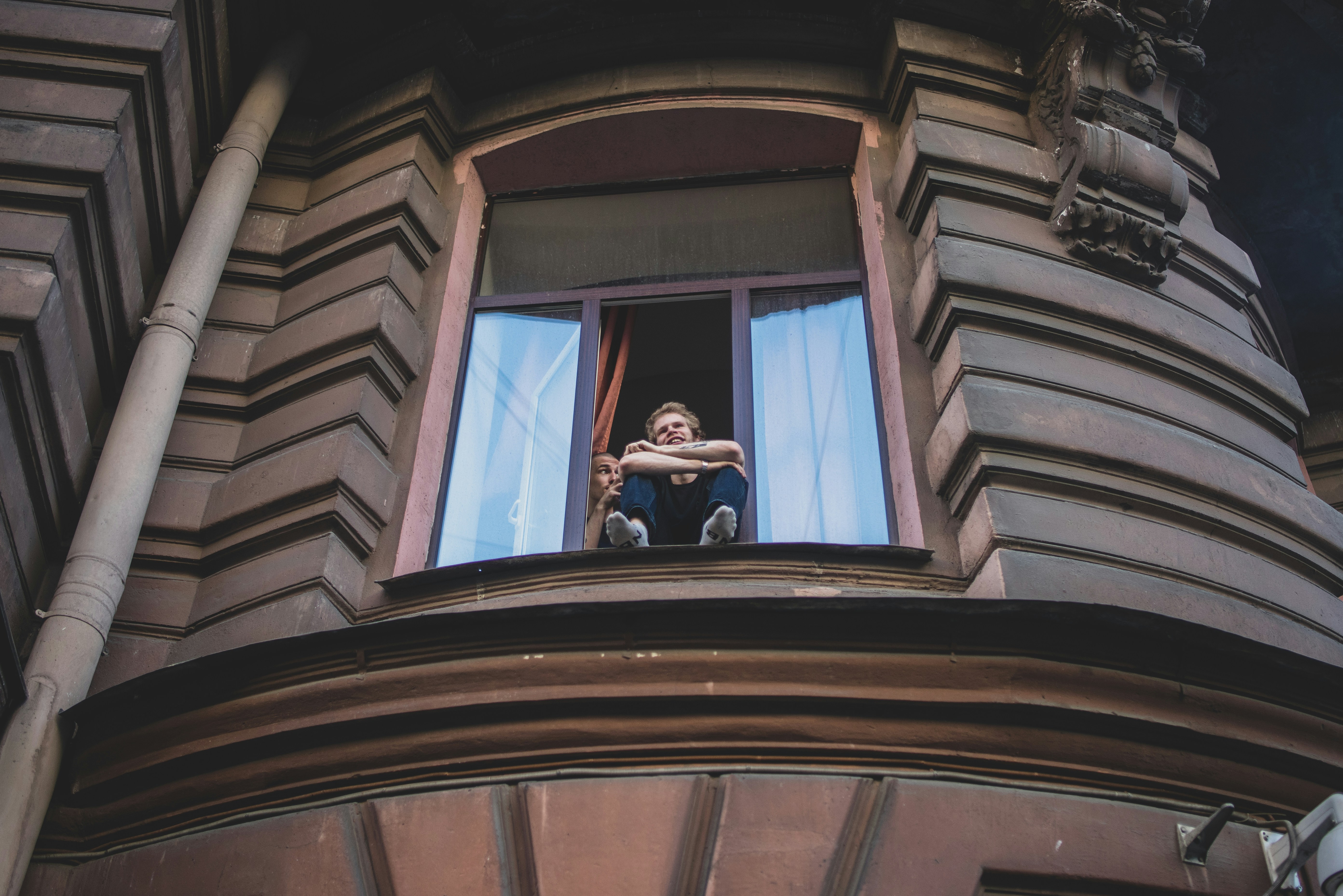 man in black t-shirt and blue denim jeans standing on brown wooden window