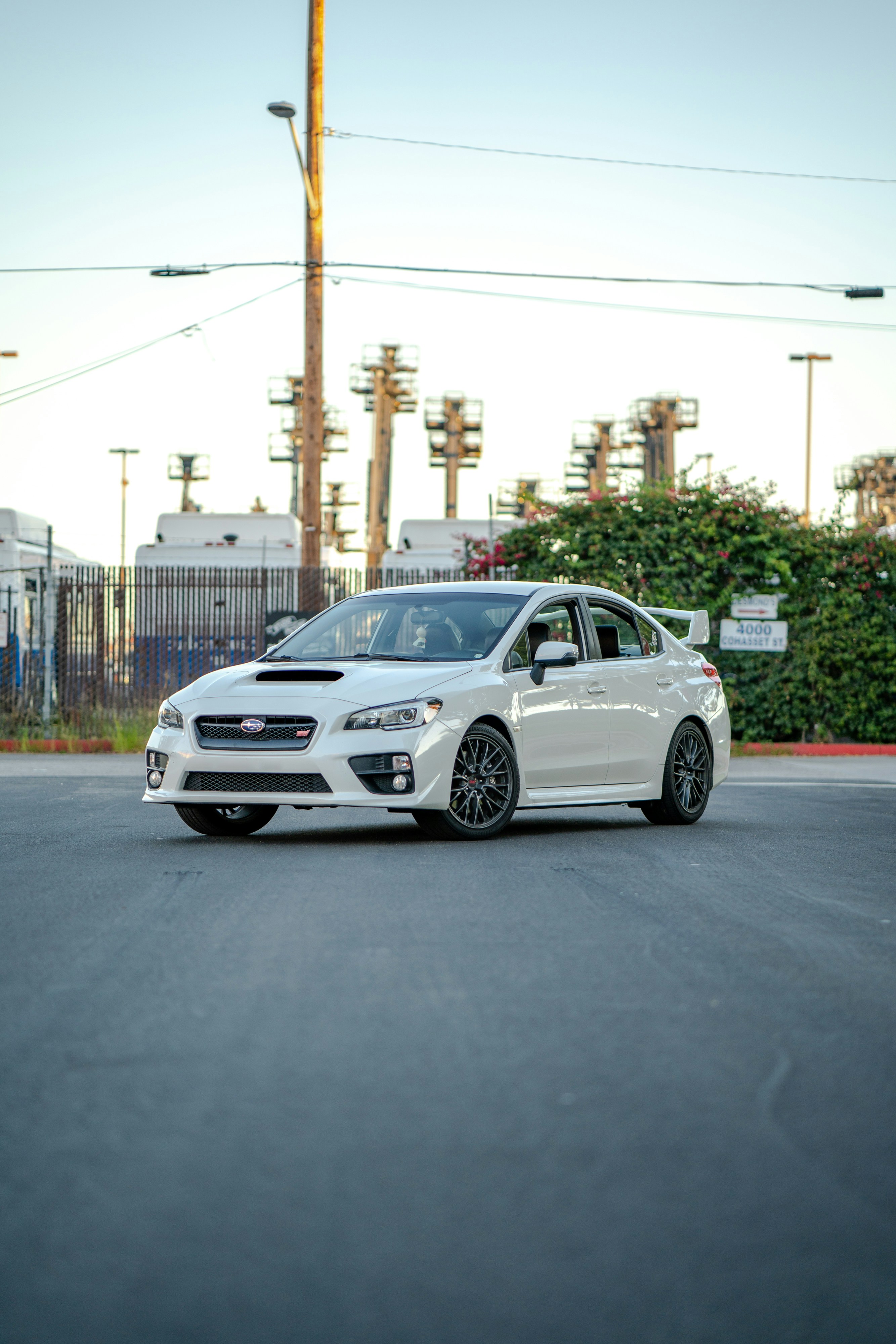 White sedan parked on a quiet street with industrial buildings in the background.