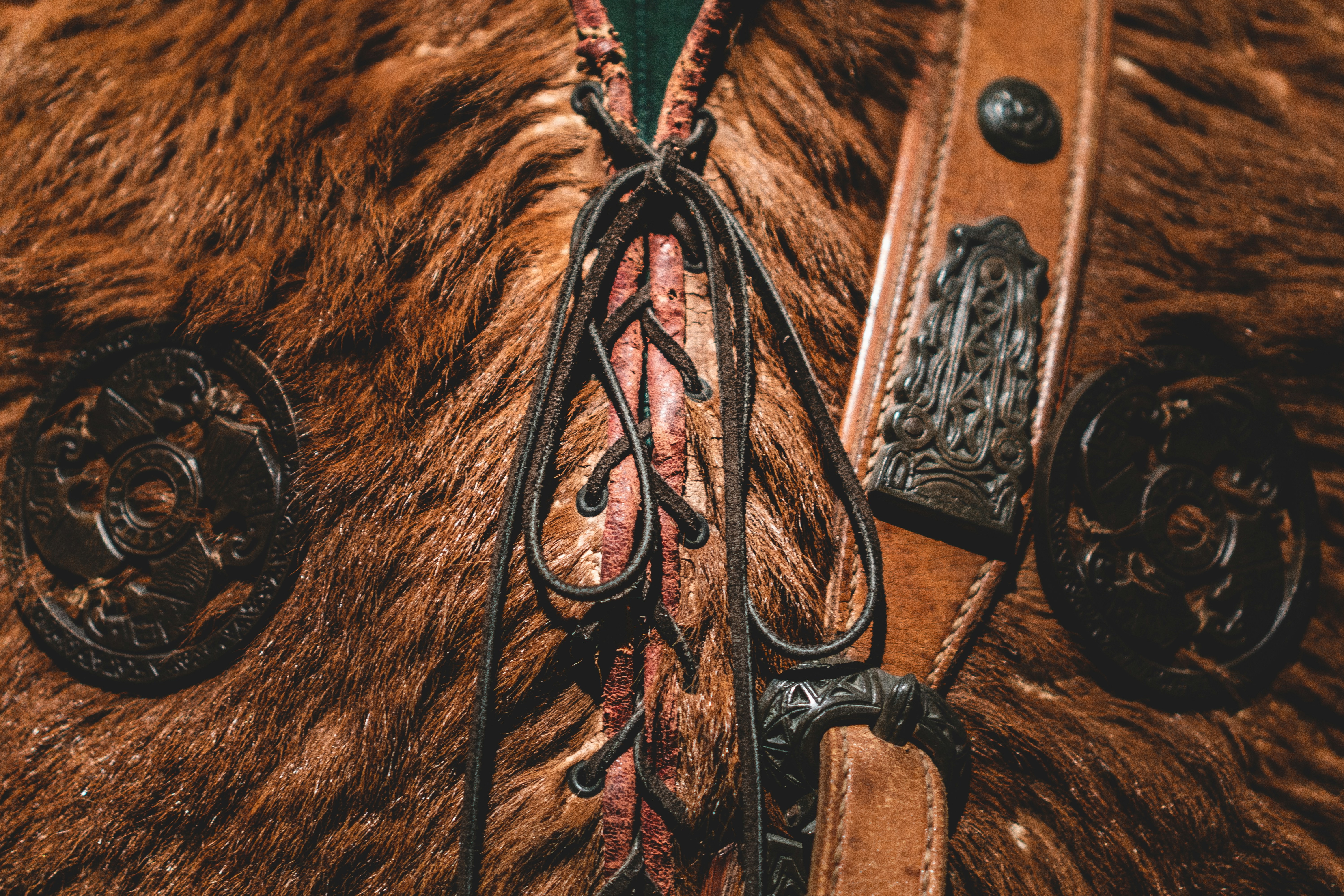 Close-up of a richly textured fur garment featuring ornate clasps and lacing. The craftsmanship highlights cultural heritage.