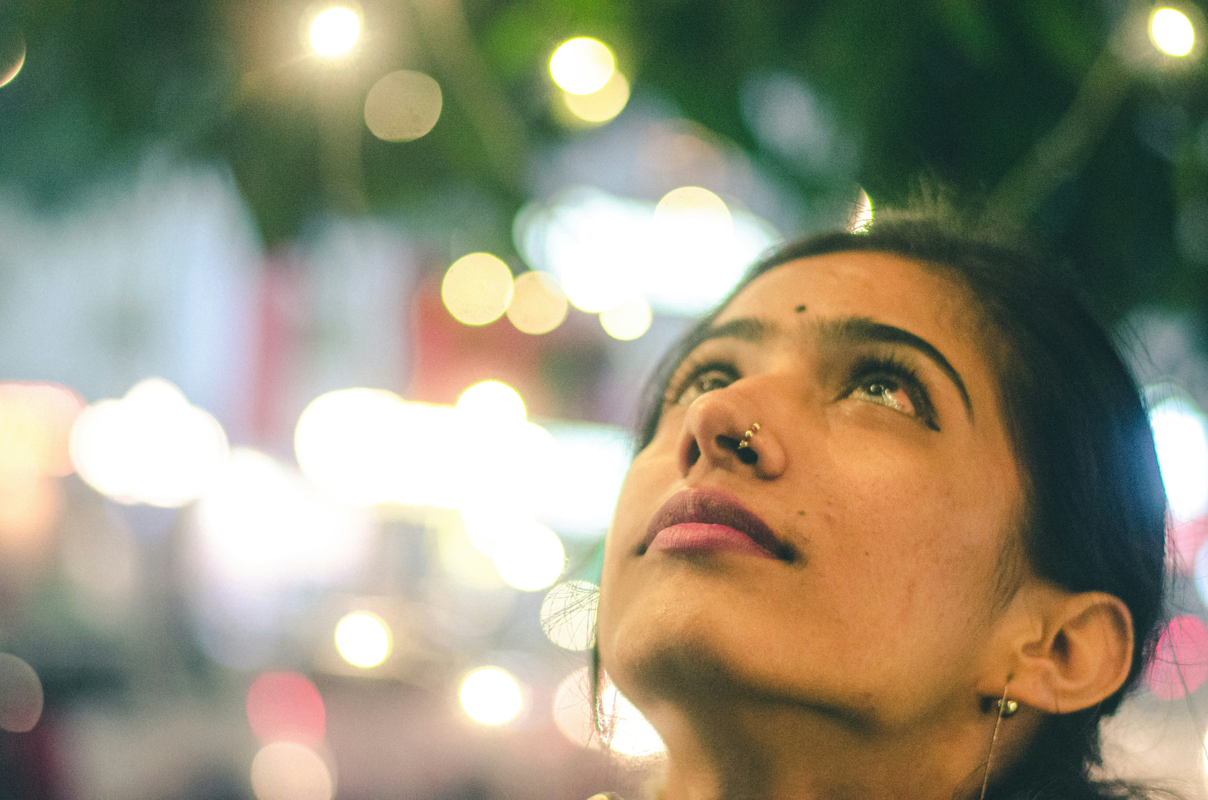 A woman gazes upward, captivated by twinkling lights overhead, with a soft bokeh effect creating a dreamy atmosphere.